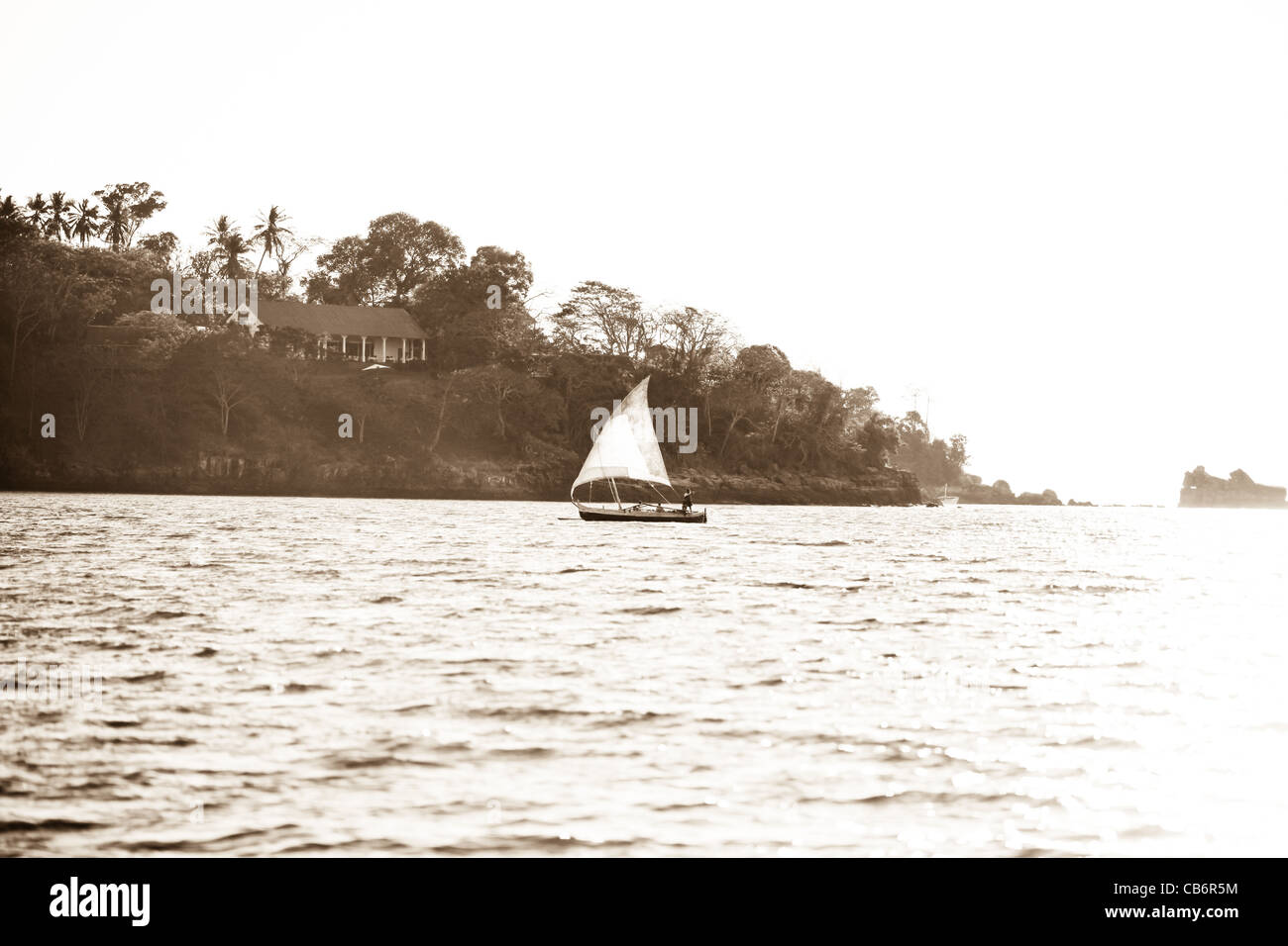 A traditional outrigger dugout canoe sailing at sunset off Ankify, near ...