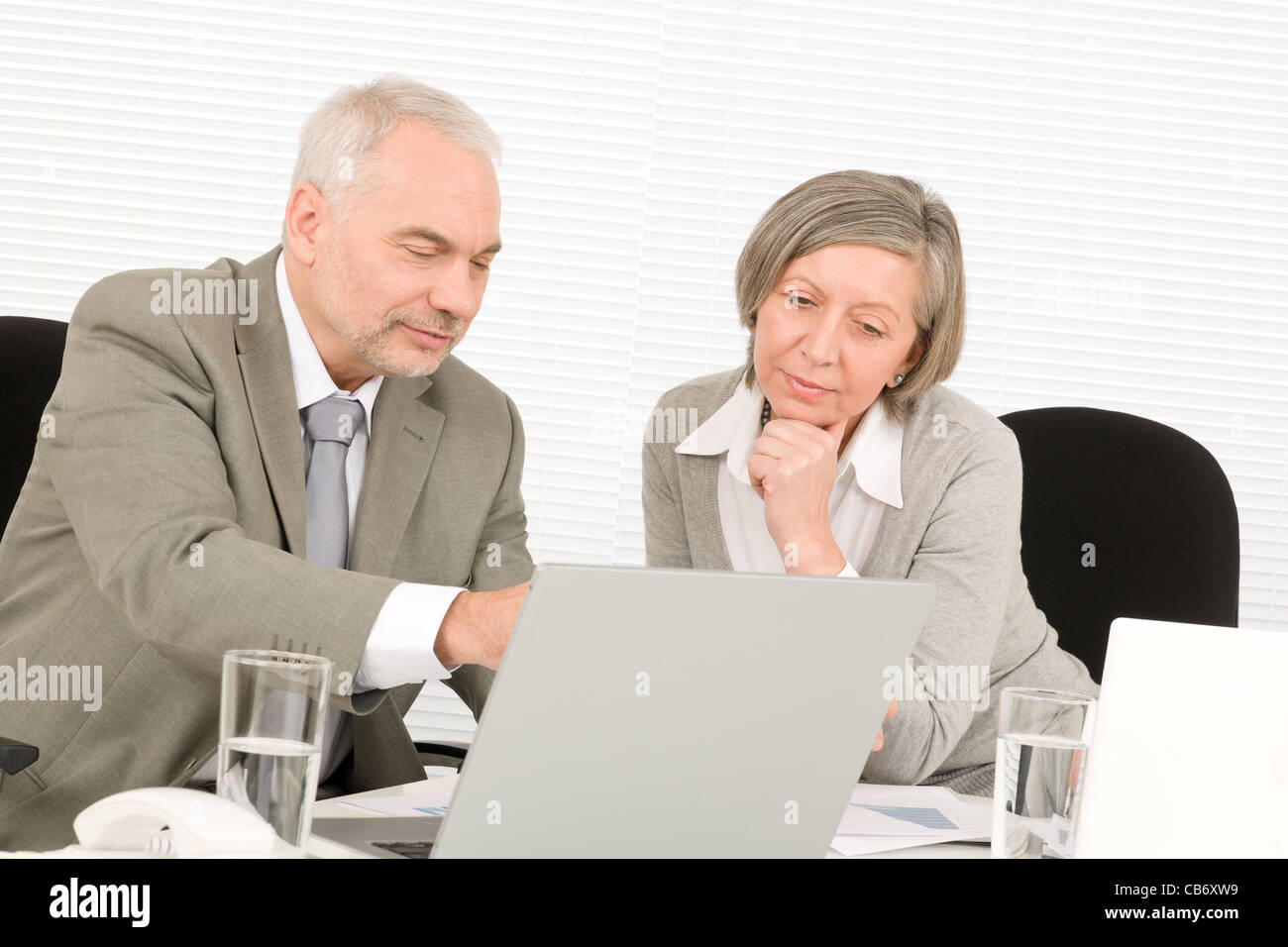 Professional senior businessman pointing at computer with woman ...