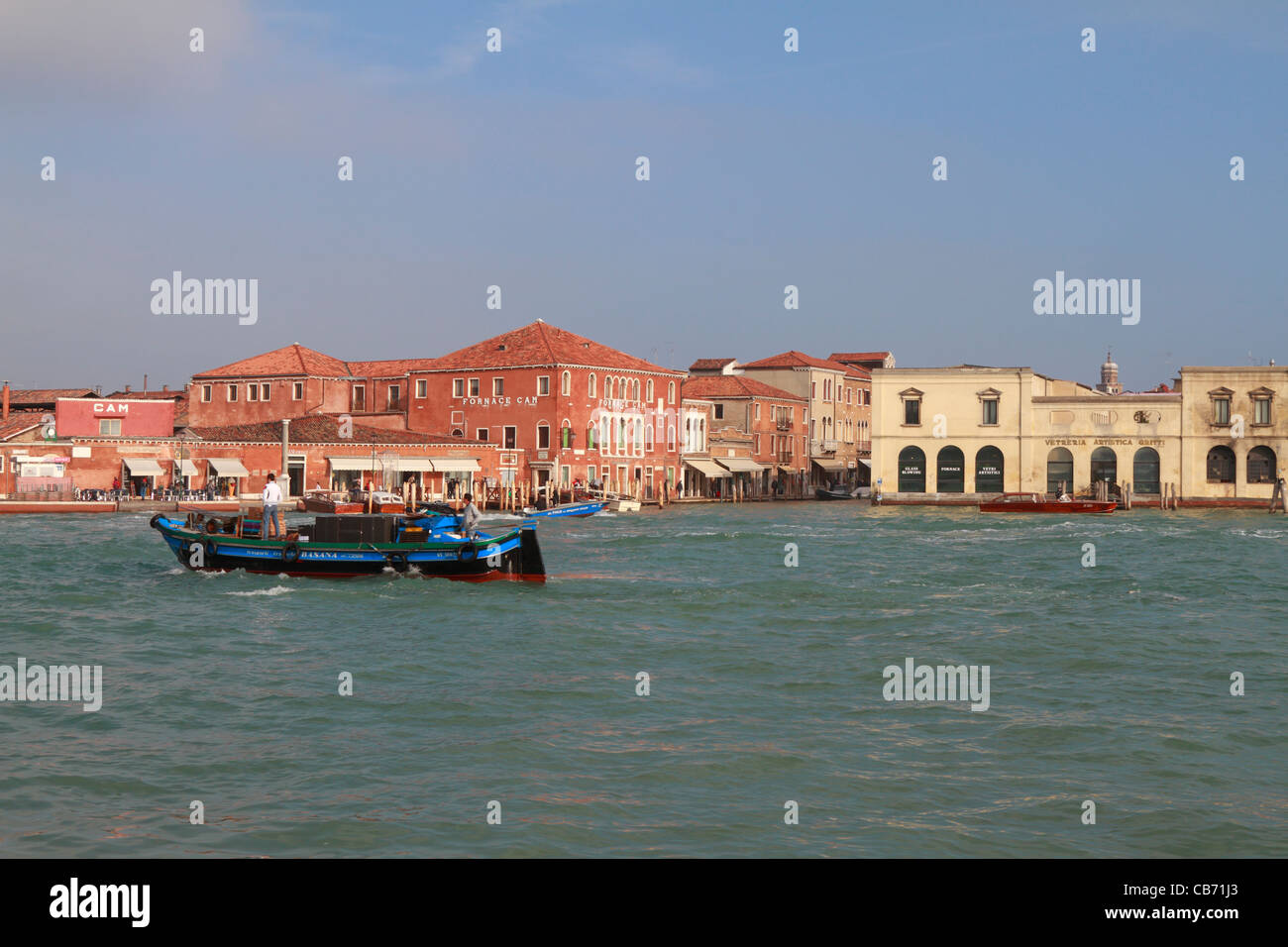 A fishing boat passes fornace glass factories, Murano, Italy, Europe ...