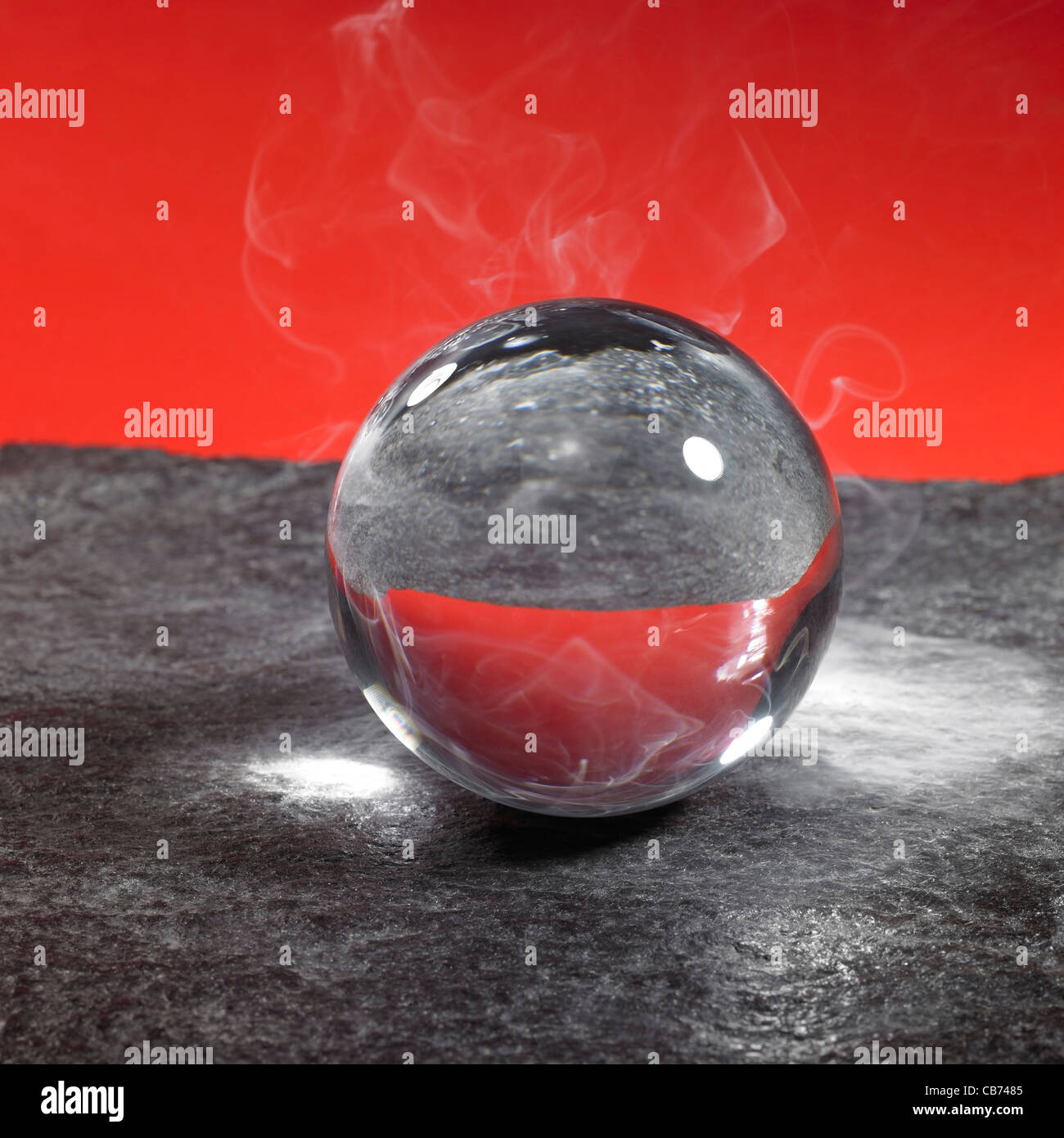 a clear crystal ball on rough dark grey stone surface in front of red ...