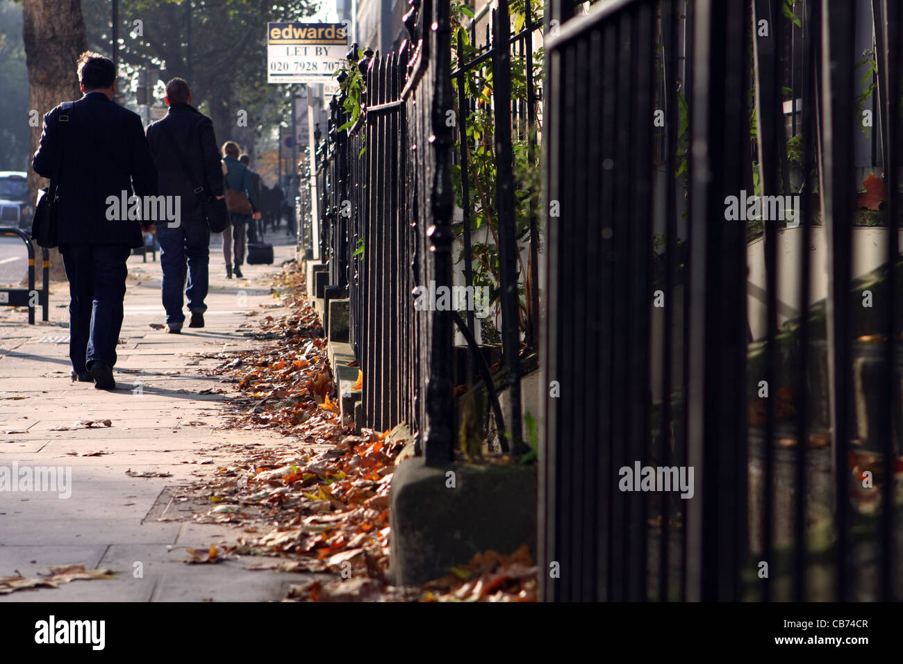 a low view along a street in London with railings on the right and ...