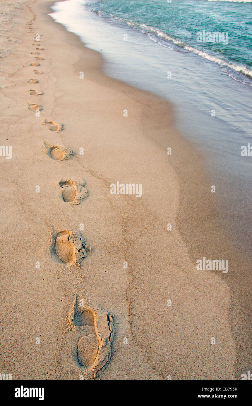 Foot imprints beside waves reaching margin at the seaside. Romantic ...