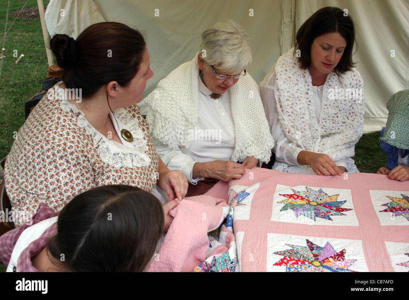 A multigenerational group of women working on a quilt in a sewing bee ...