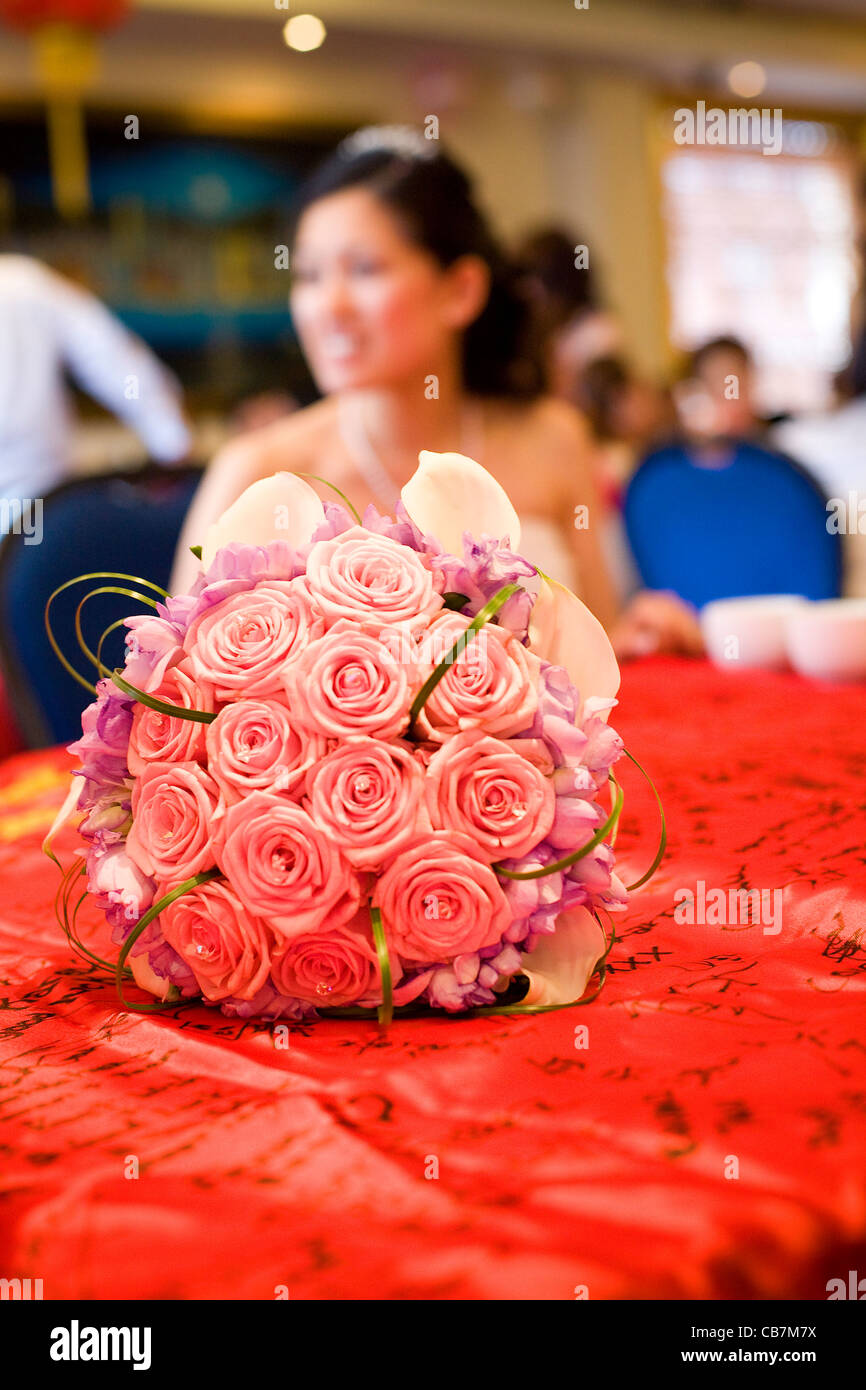 A Chinese bride is smiling behind wedding bouquet made off pink roses ...