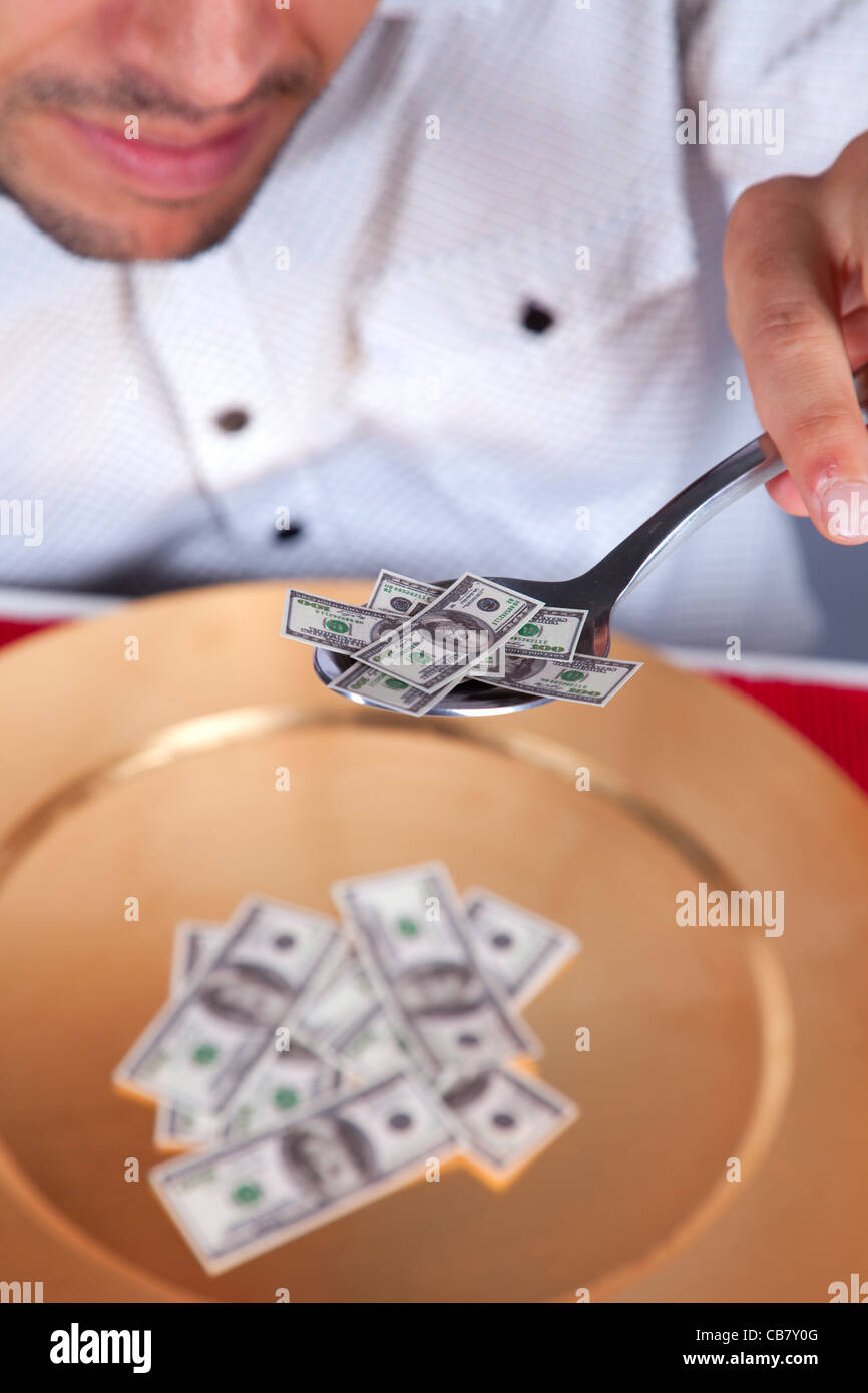 Man eating money at a plate with a fork and a knife Stock Photo - Alamy