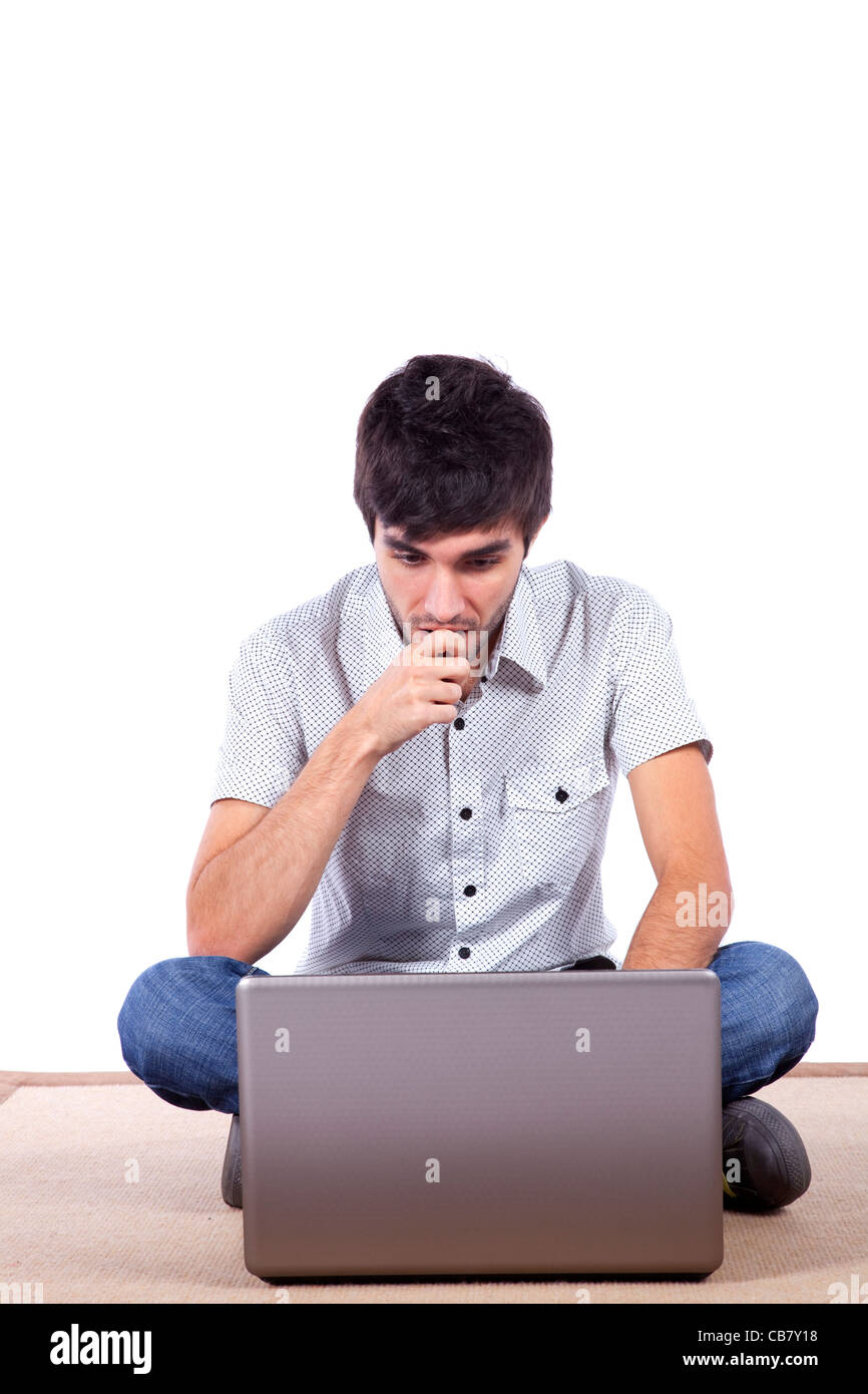young man surfing the internet in his laptop sited on the carpet ...