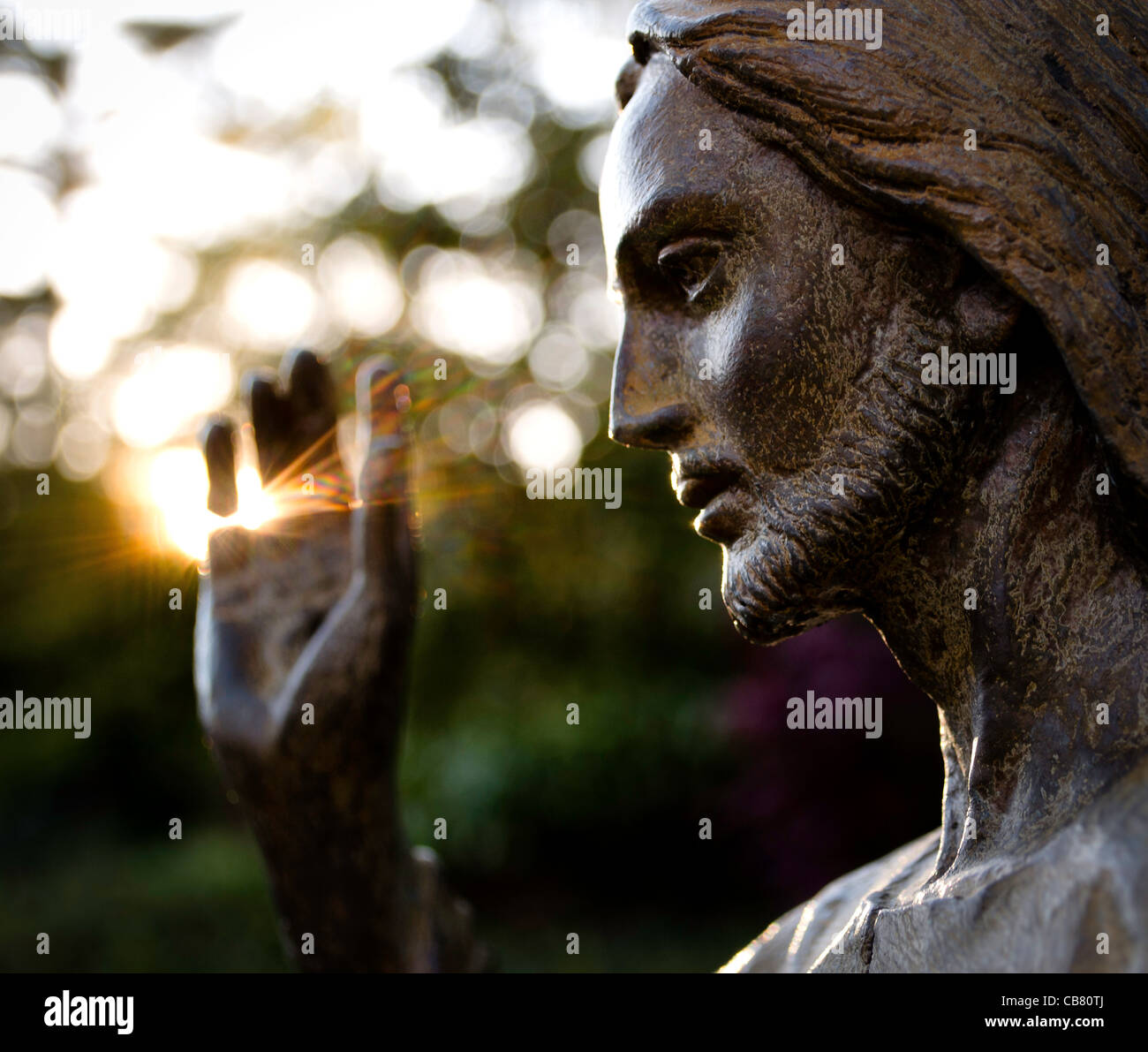 Sunrise in spring sparks rays of light into the hand of a statue of ...