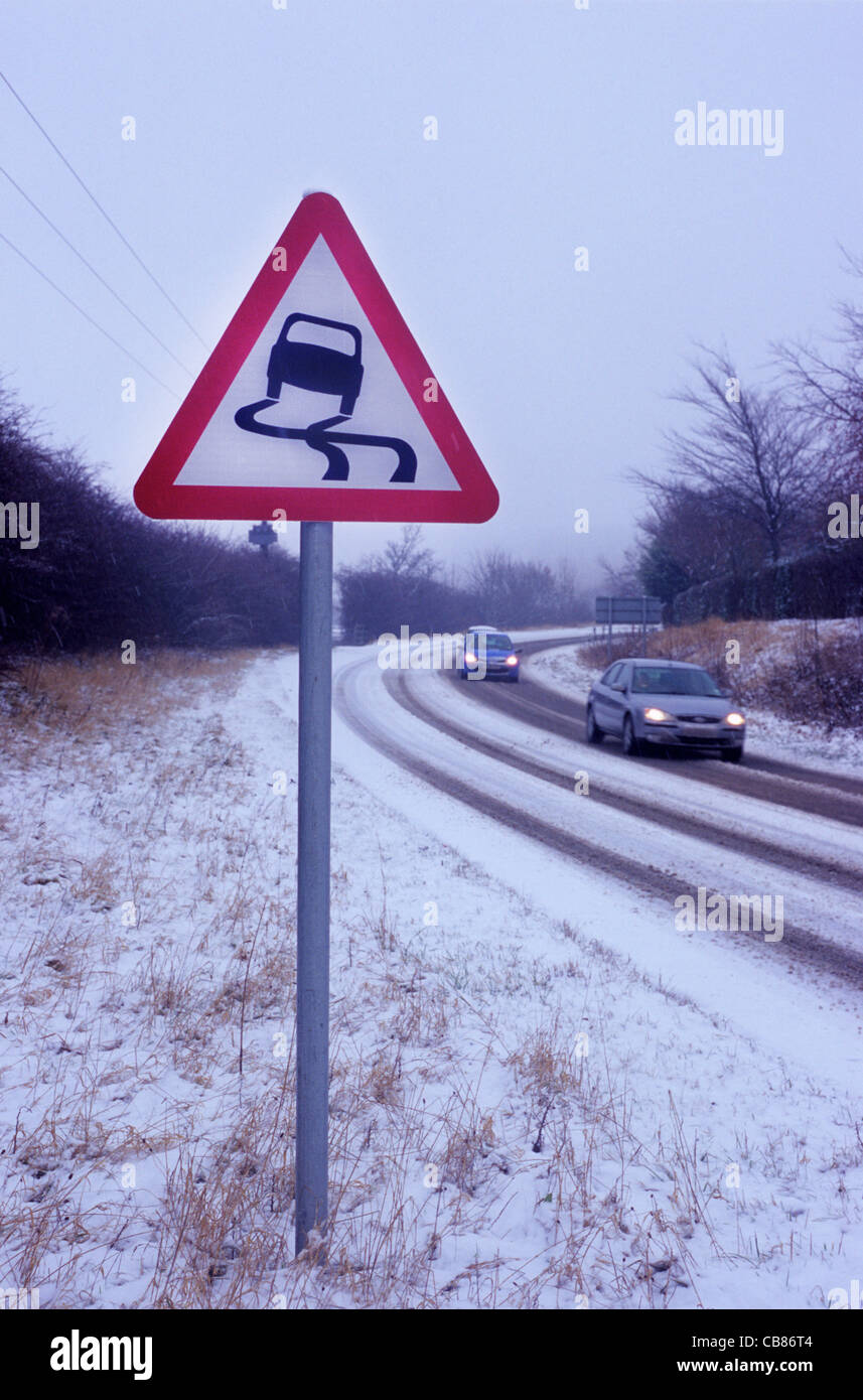car travelling in winter snow passing warning sign of icy road near ...