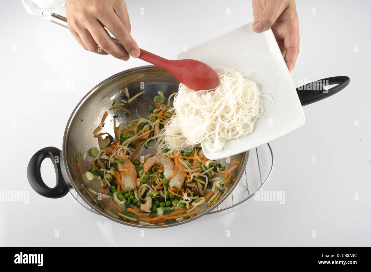 Adding noodles to a wok with vegetables Stock Photo - Alamy