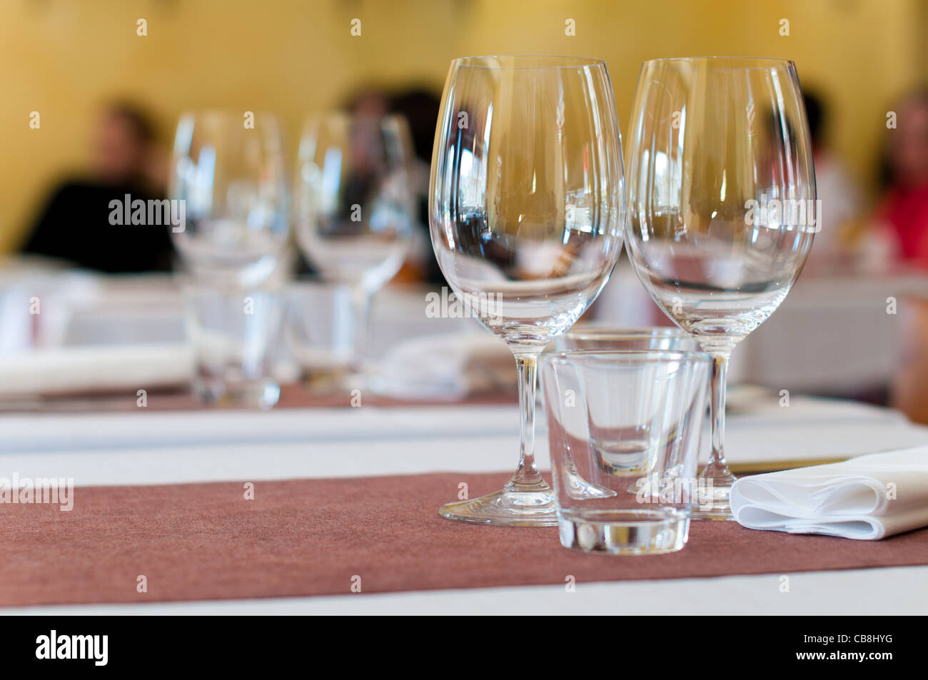 two empty glass goblets on table in restaurant with visitors in ...