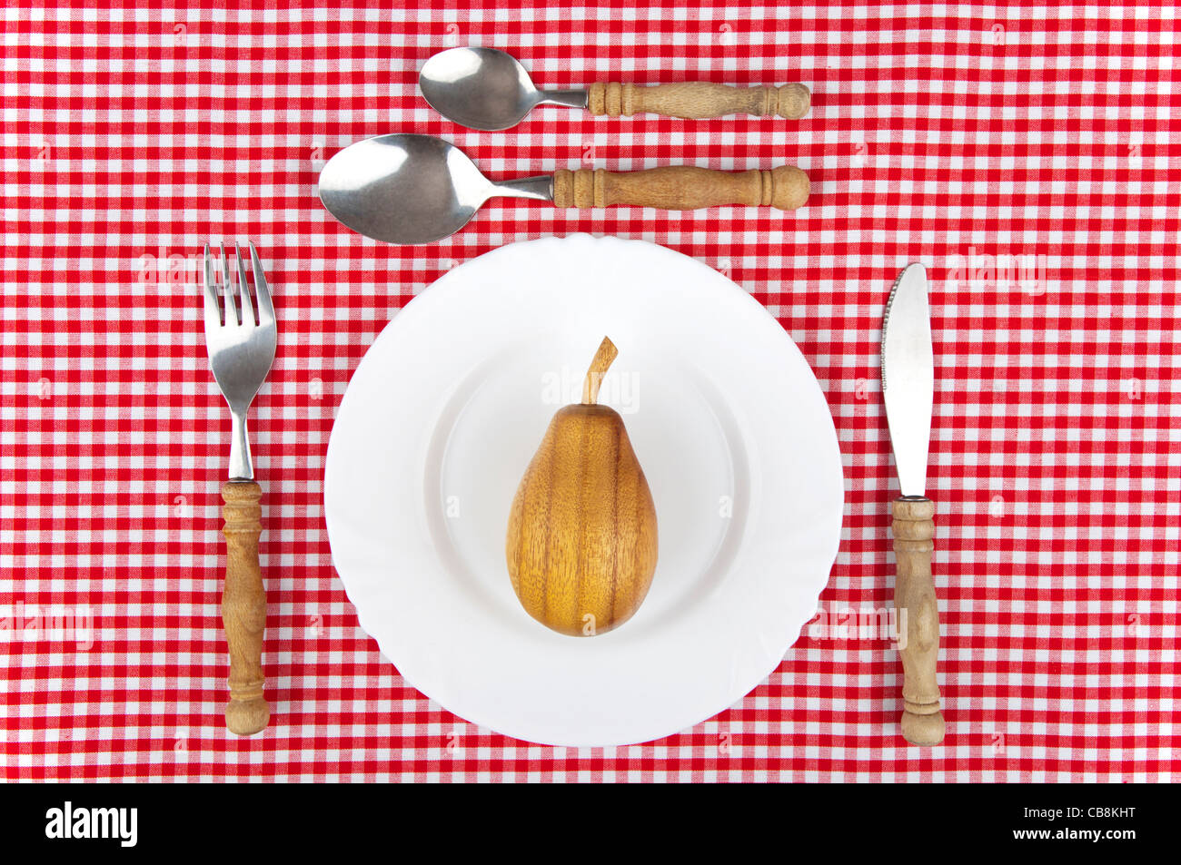 white plate on checkered tablecloth with flatware and wooden pear Stock ...