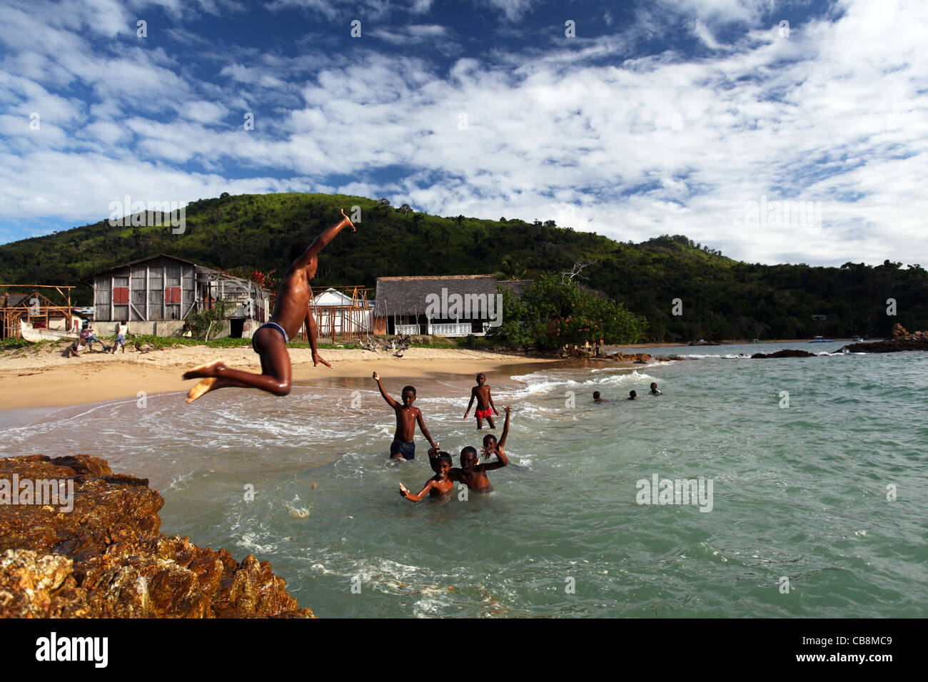 A group of malagasy local boys at the beach, one of them jumping into ...