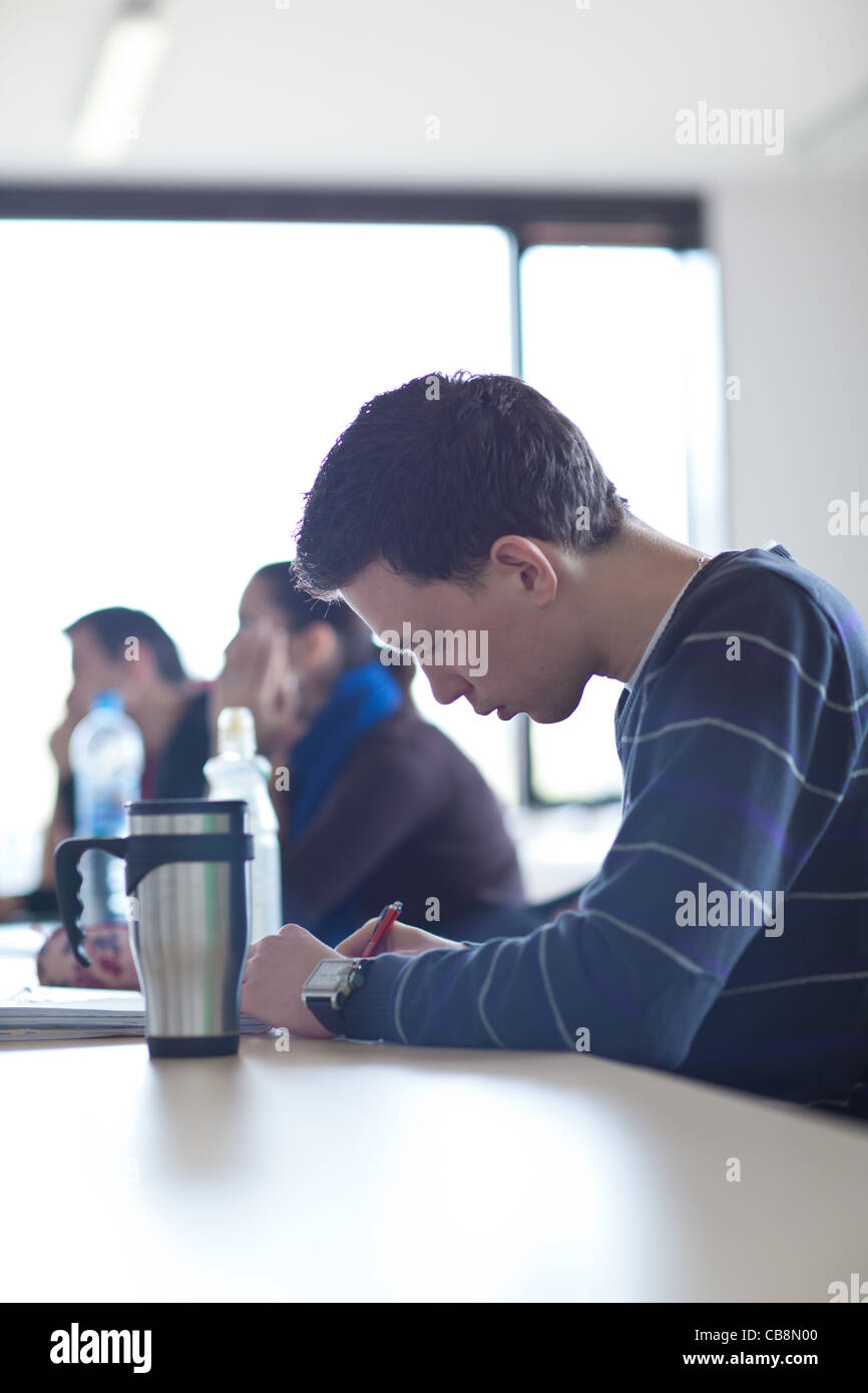 young, handsome male college student sitting in a classroom full of ...
