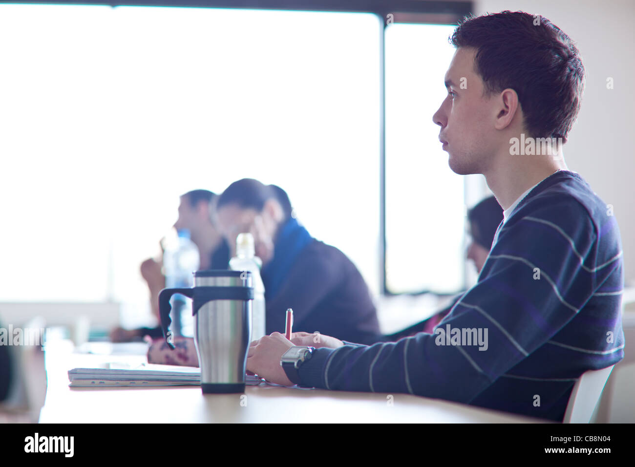 young, handsome male college student sitting in a classroom full of ...