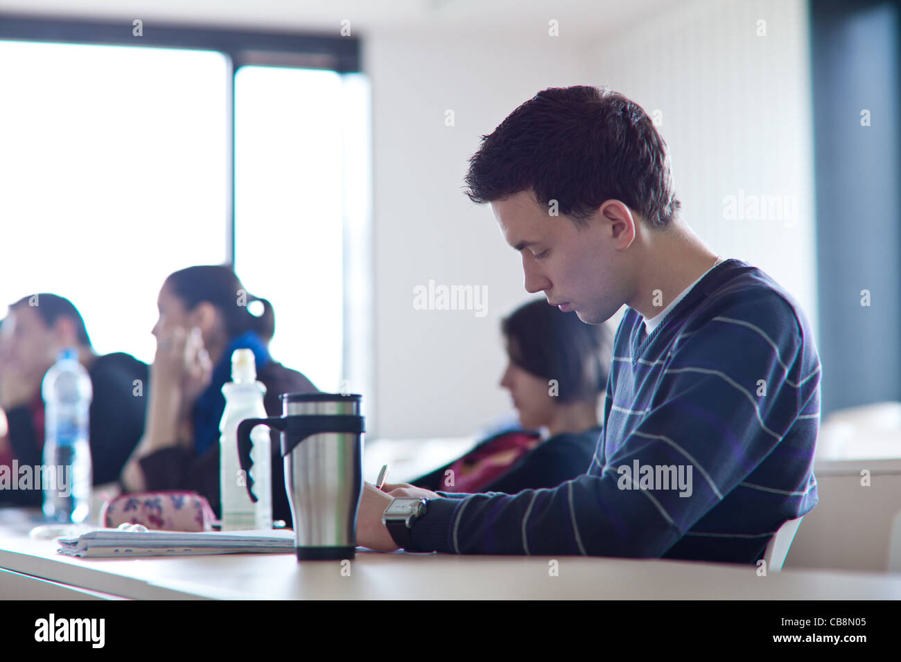 young, handsome male college student sitting in a classroom full of ...