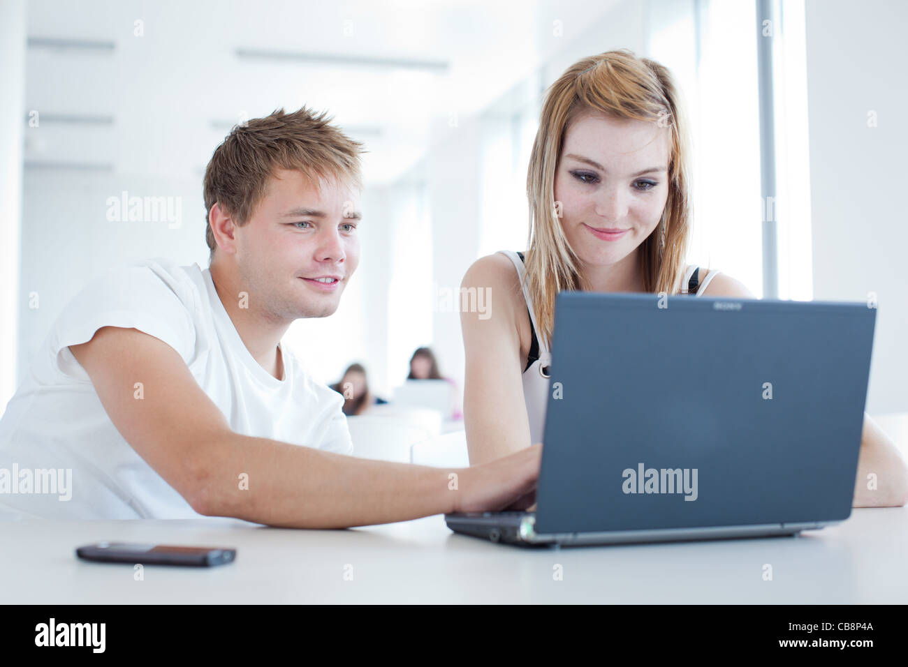 two college students having fun studying together, using a laptop ...