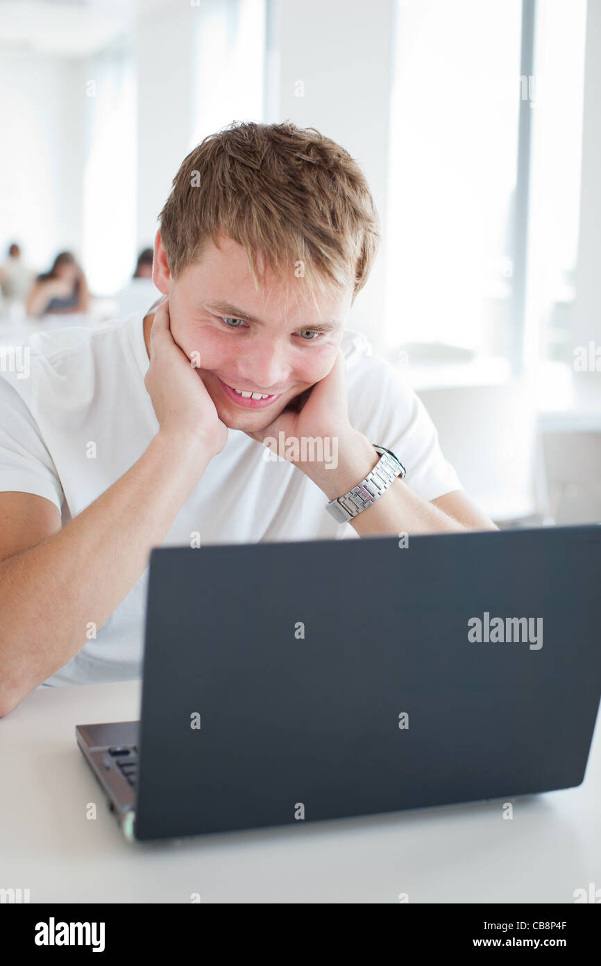 Young male college student working on his laptop computer in a ...