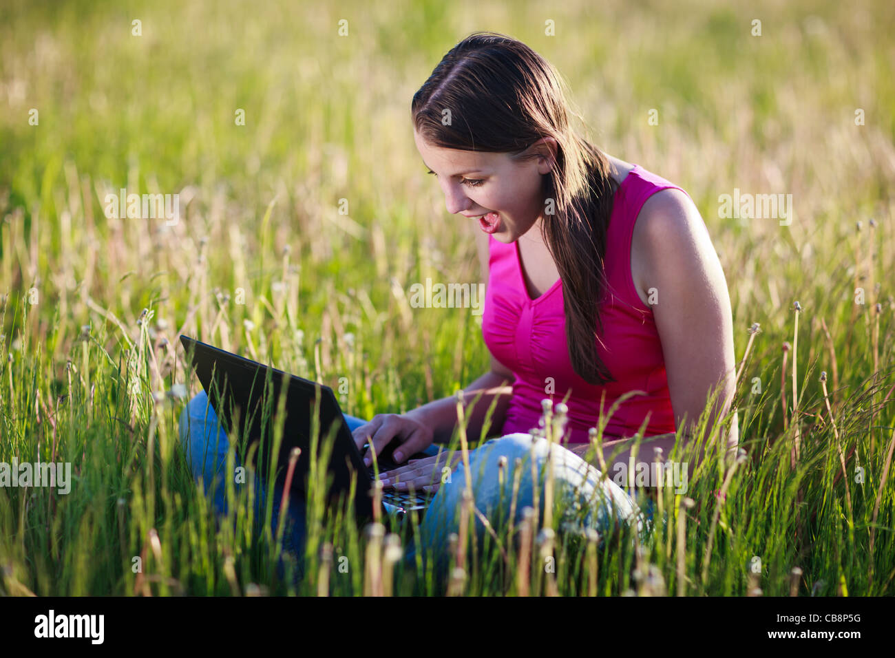 pretty , young woman using her laptop computer outdoors in the middle ...