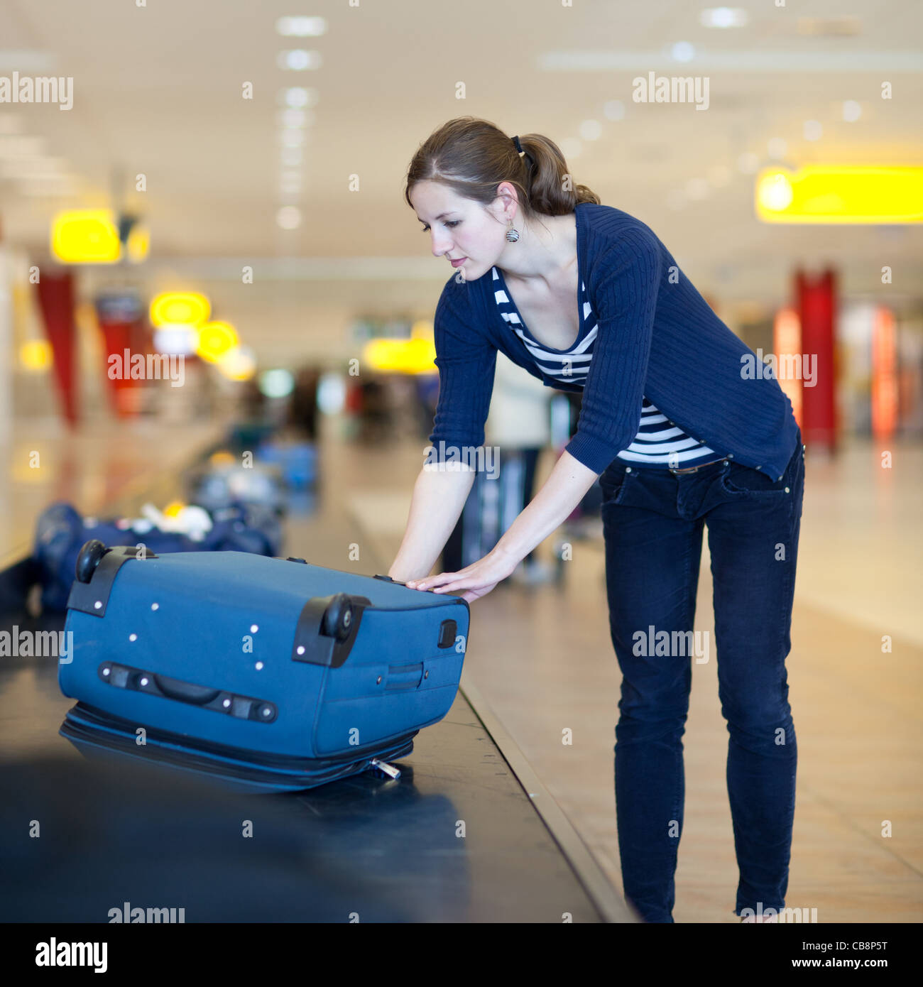 Baggage reclaim at the airport - pretty young woman taking her suitcase ...
