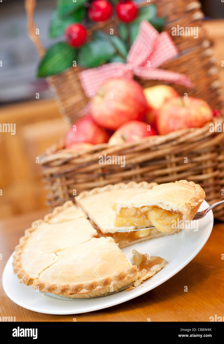 Apple pie on a wooden table with a basket of apples in background Stock ...