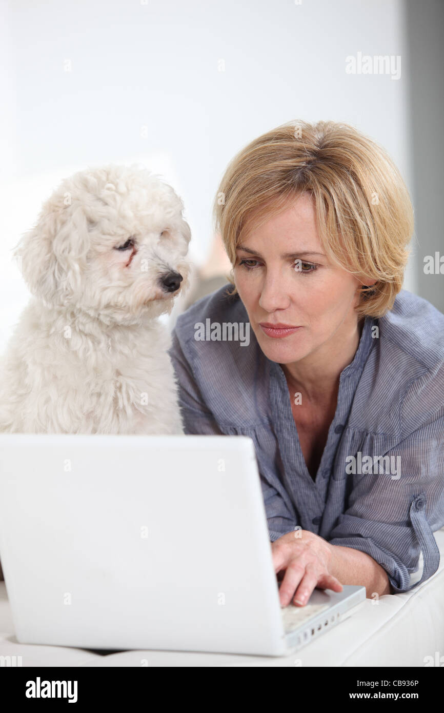 Woman typing on laptop computer next to small white dog Stock Photo - Alamy