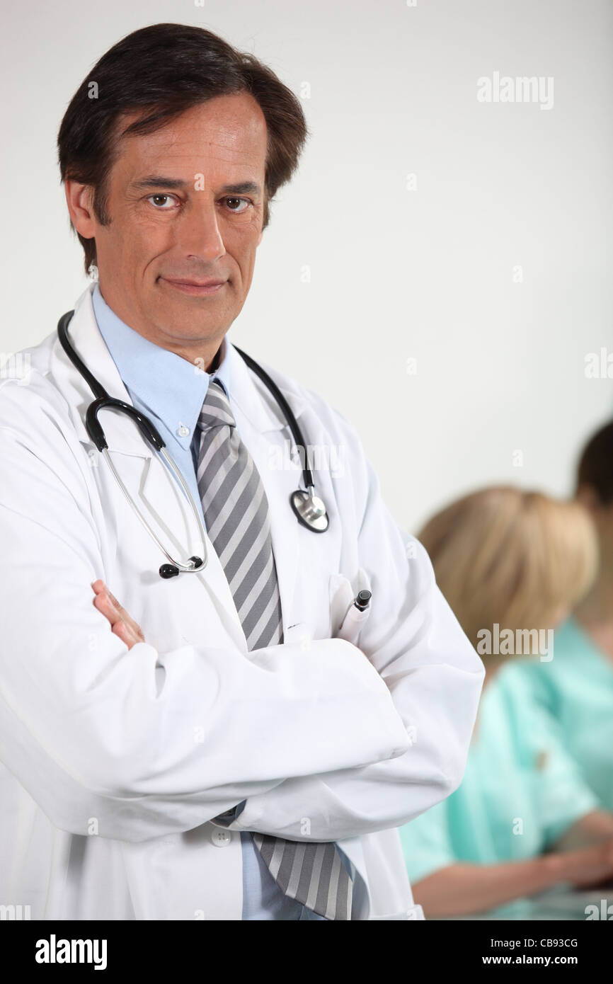 Male doctor stood with arms folded colleagues in background Stock Photo ...