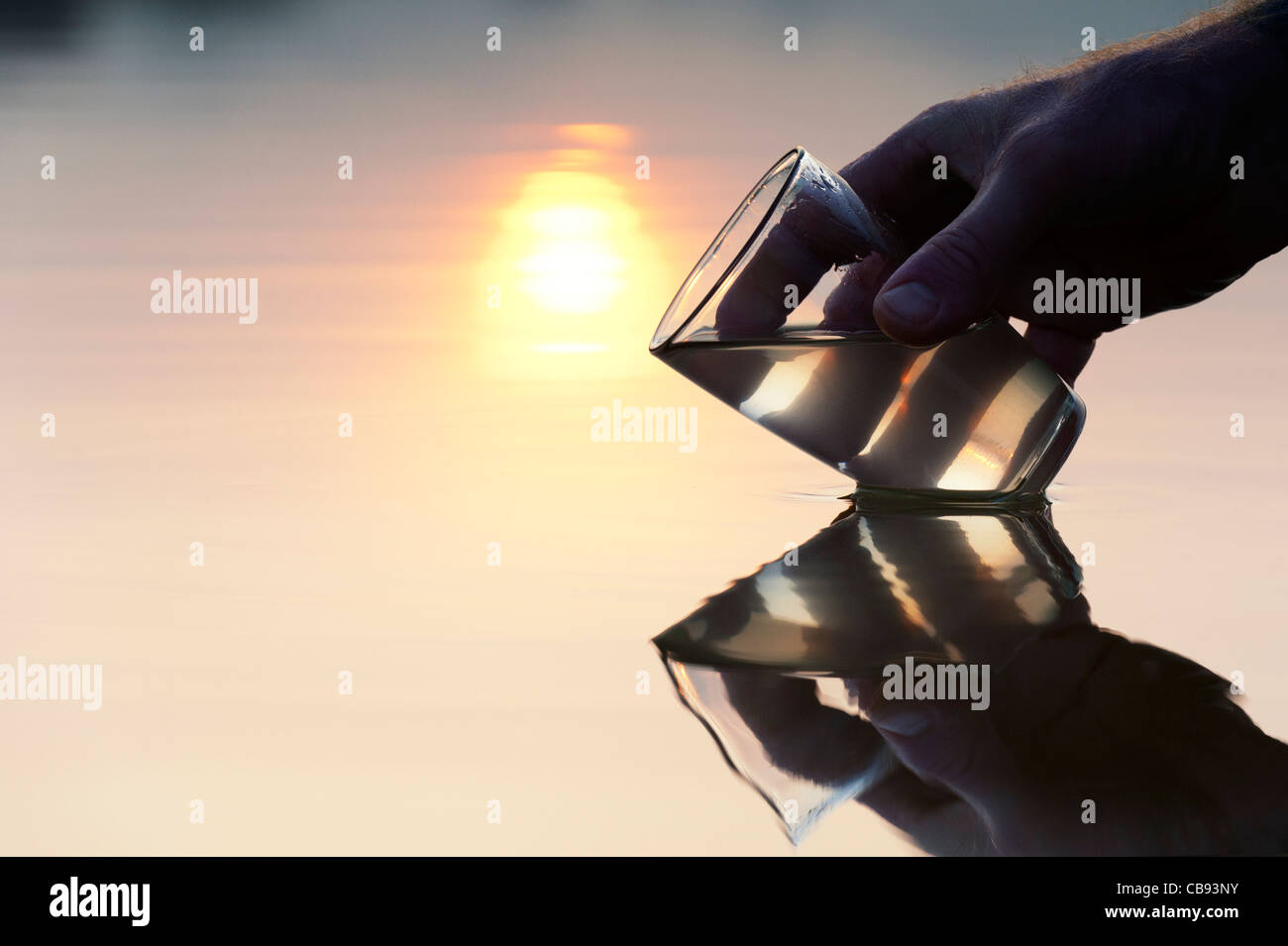 Hand scooping up water in a glass into a still lake at sunrise in India ...
