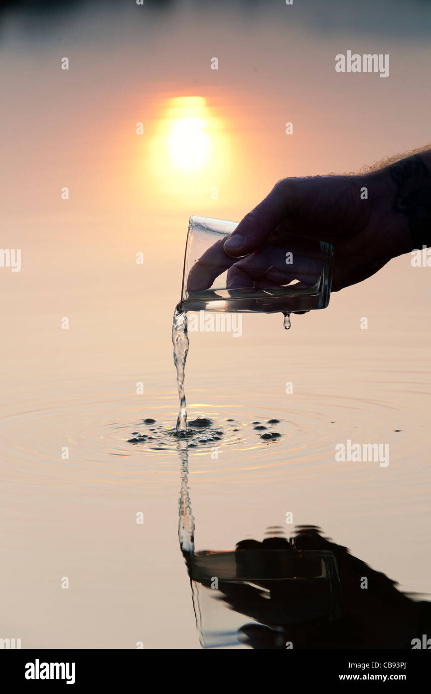 Pouring water from a glass into a still lake at sunrise in India ...
