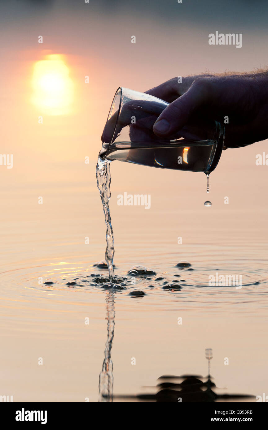 Pouring water from a glass into a still lake at sunrise in India ...