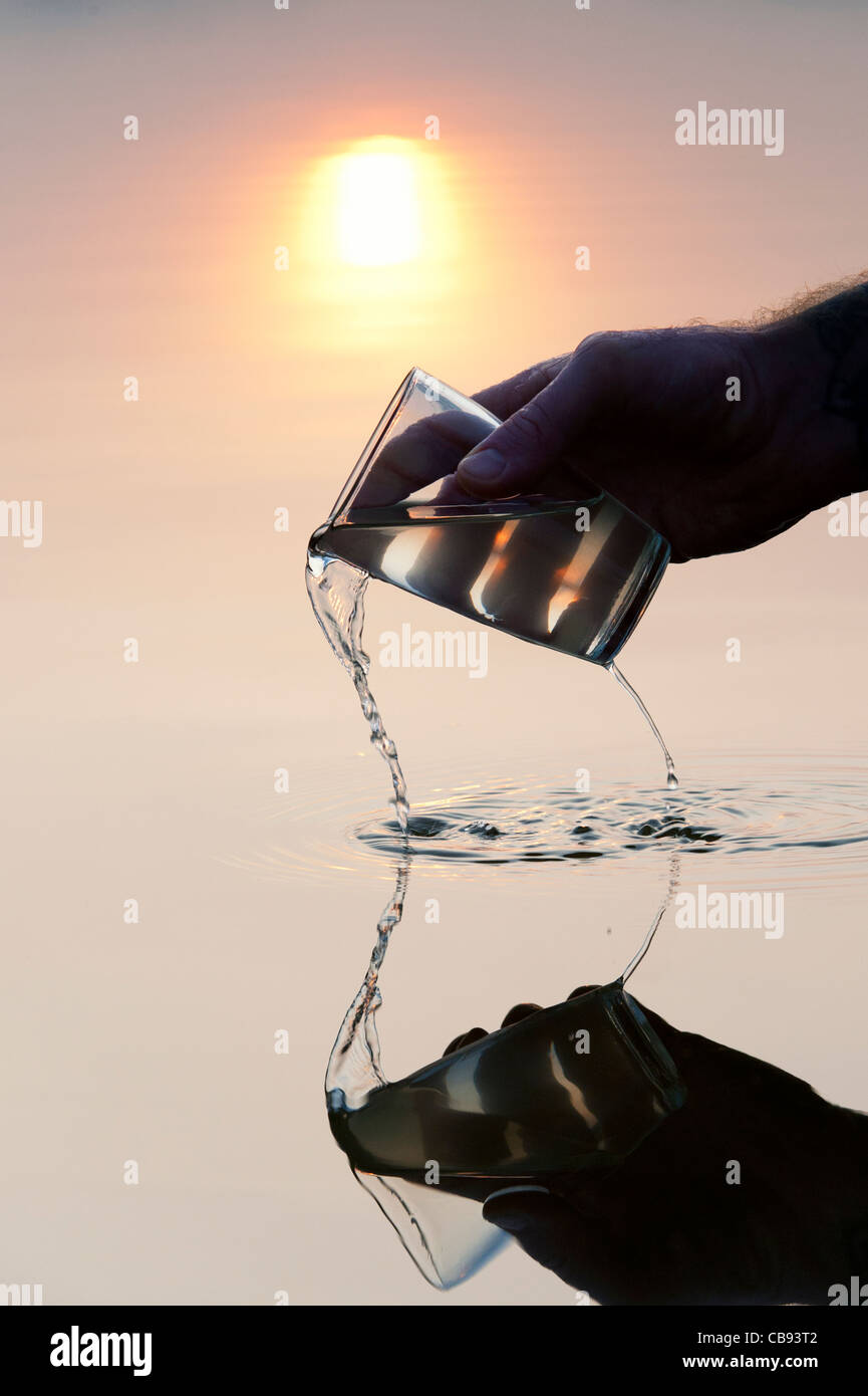 Pouring water from a glass into a still lake at sunrise in India ...