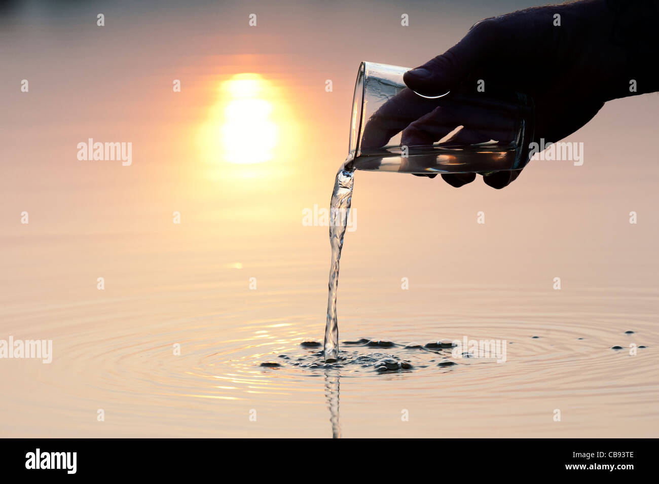 Pouring water from a glass into a still lake at sunrise in India ...