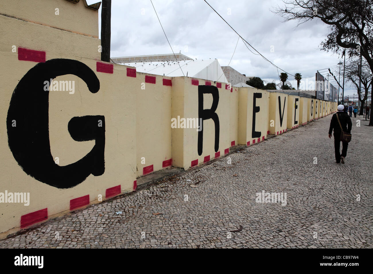 A man walks along a pavement past a sign for "Greve Geral" (meaning ...