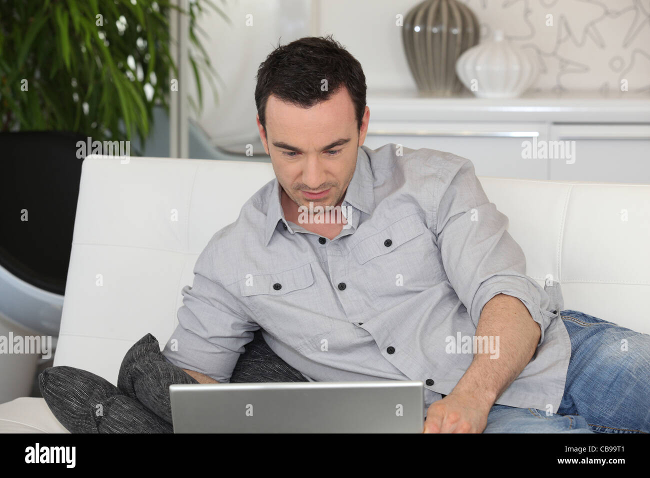 Man using a laptop on a sofa Stock Photo - Alamy