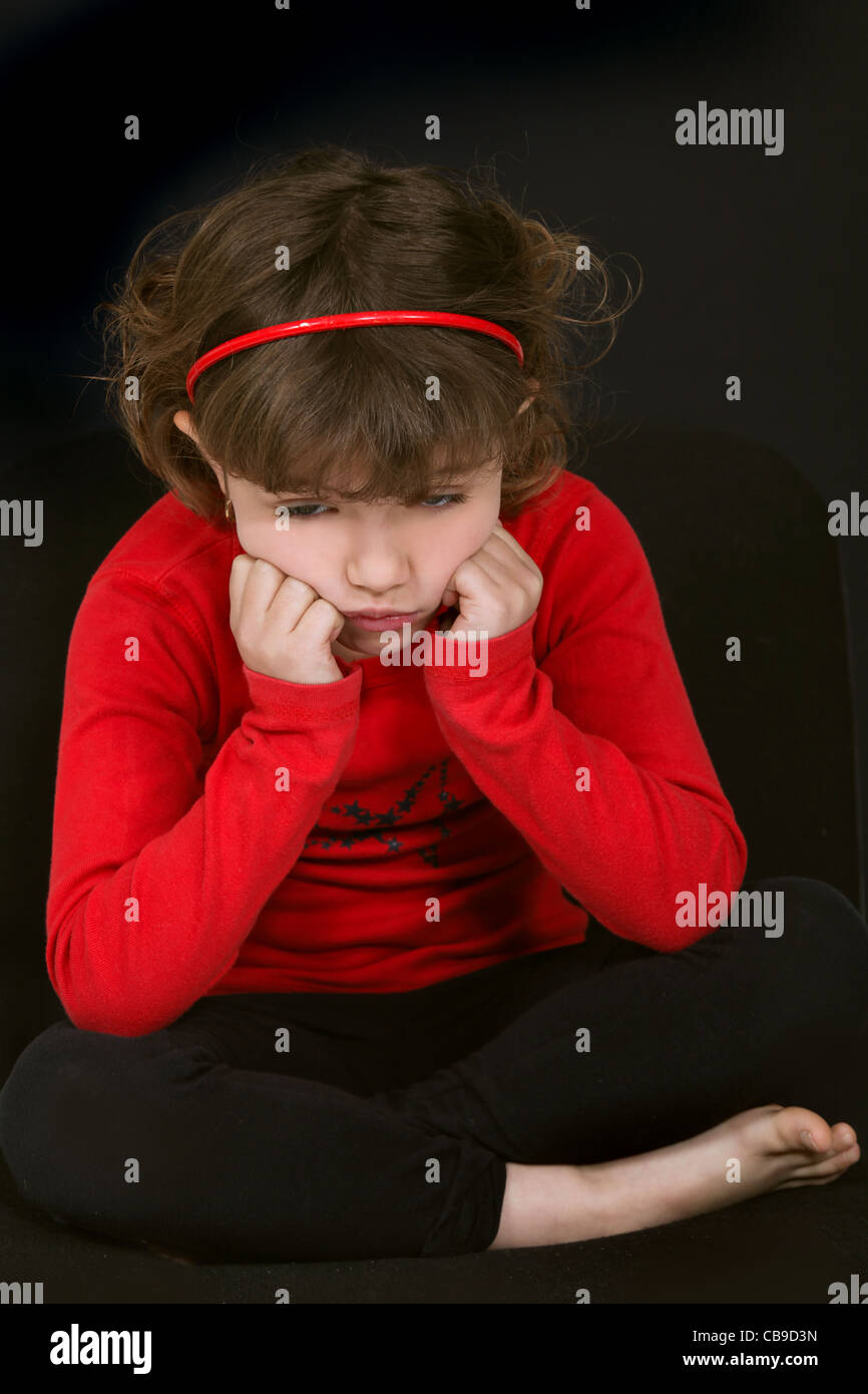 little girl pouting with face resting on hands against black background ...