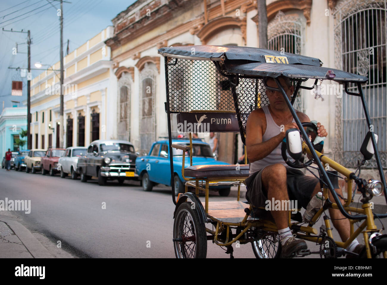 Bicycle rickshaw driver passing by, old American cars in the background ...