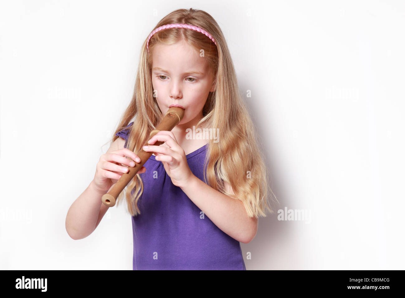 Little girl in purple dress playing recorder against white background ...