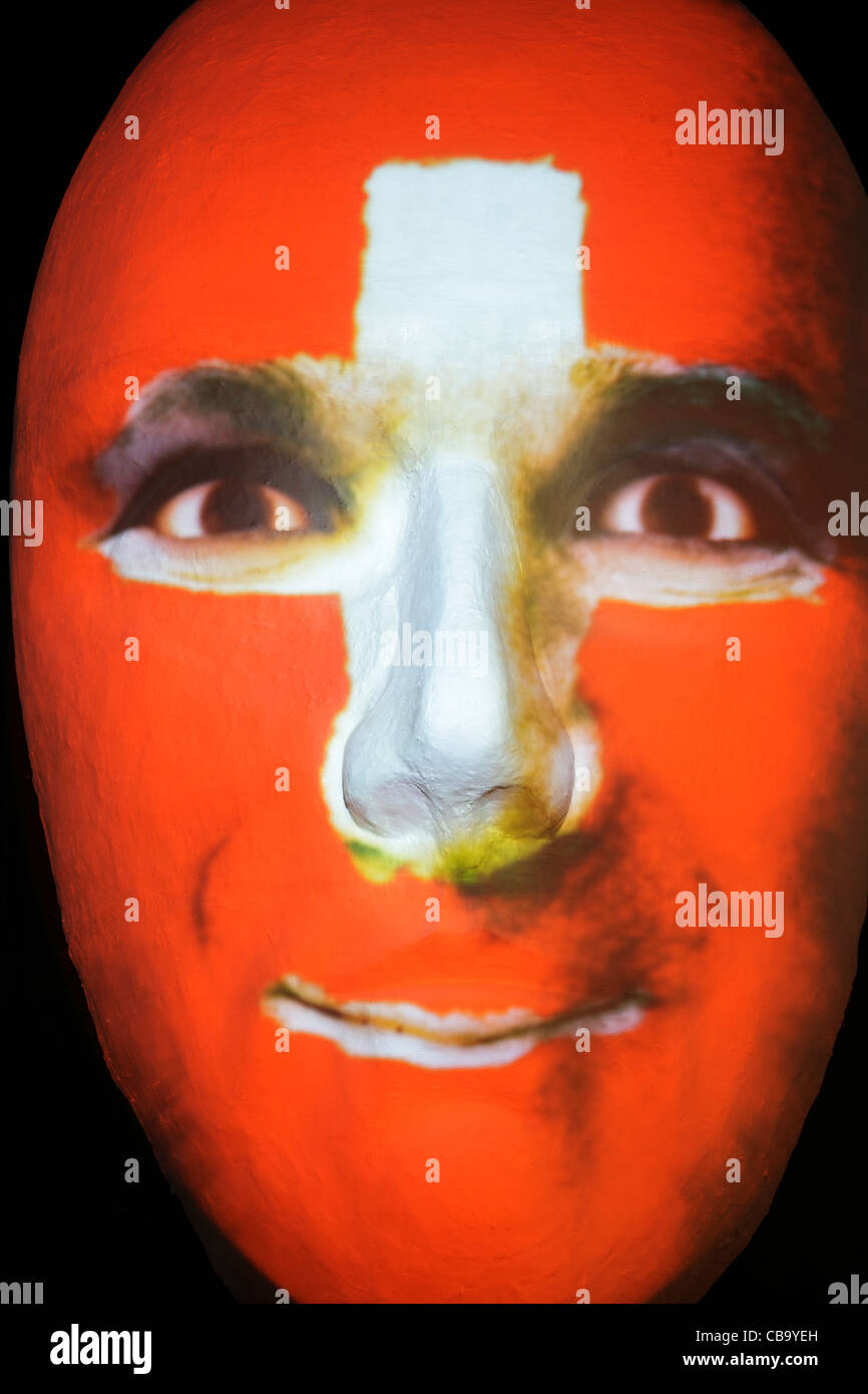 Huge sculpture of a face illuminated by an image of a Swiss flag ...