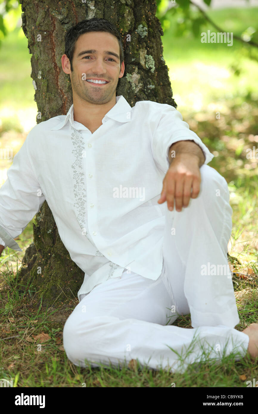 Man in white relaxing against a tree Stock Photo - Alamy