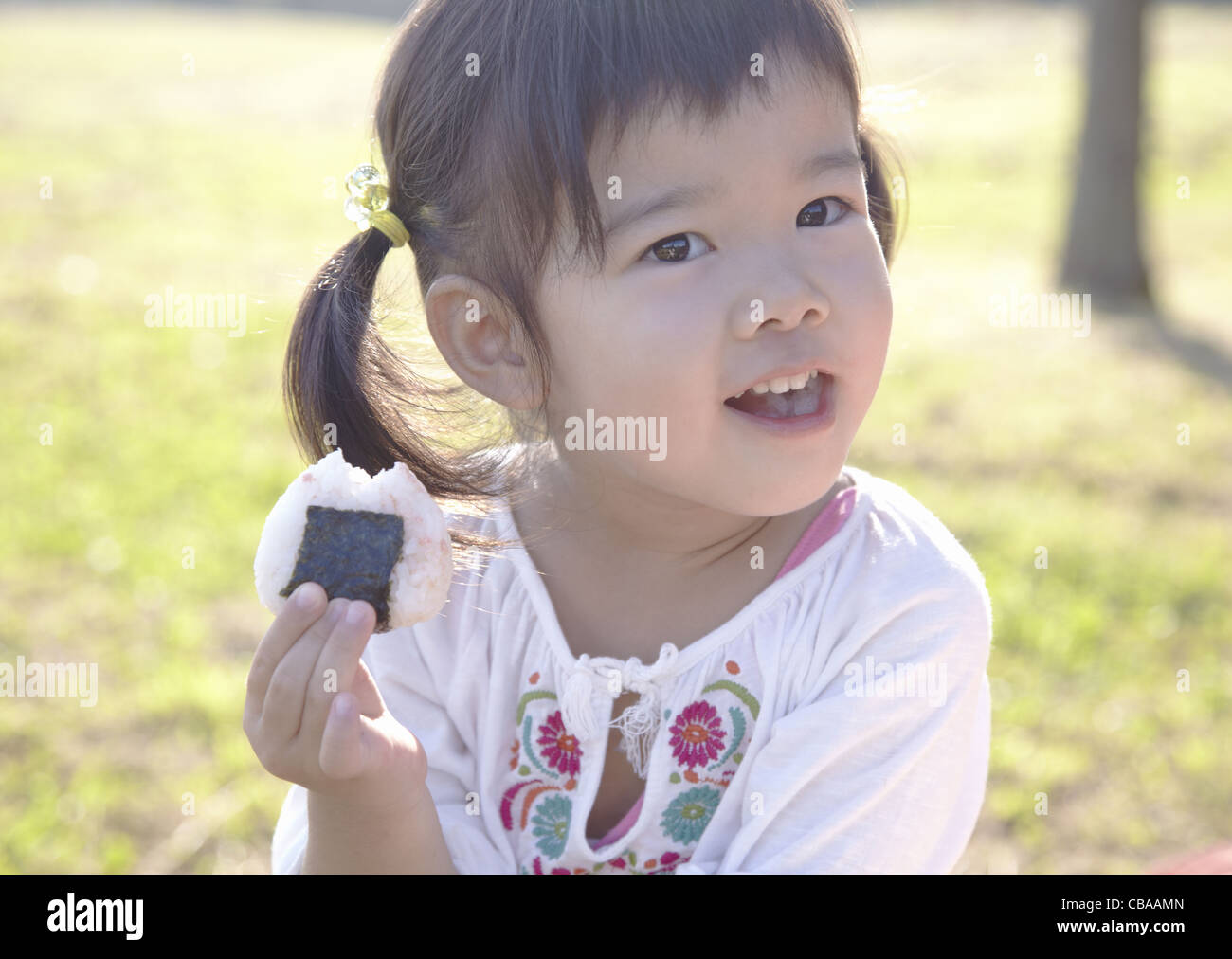 Girl eating rice ball in a park Stock Photo - Alamy
