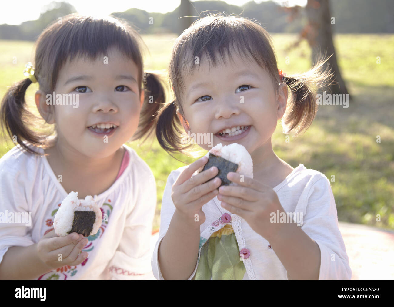 Two girls eating rice balls in a park Stock Photo - Alamy