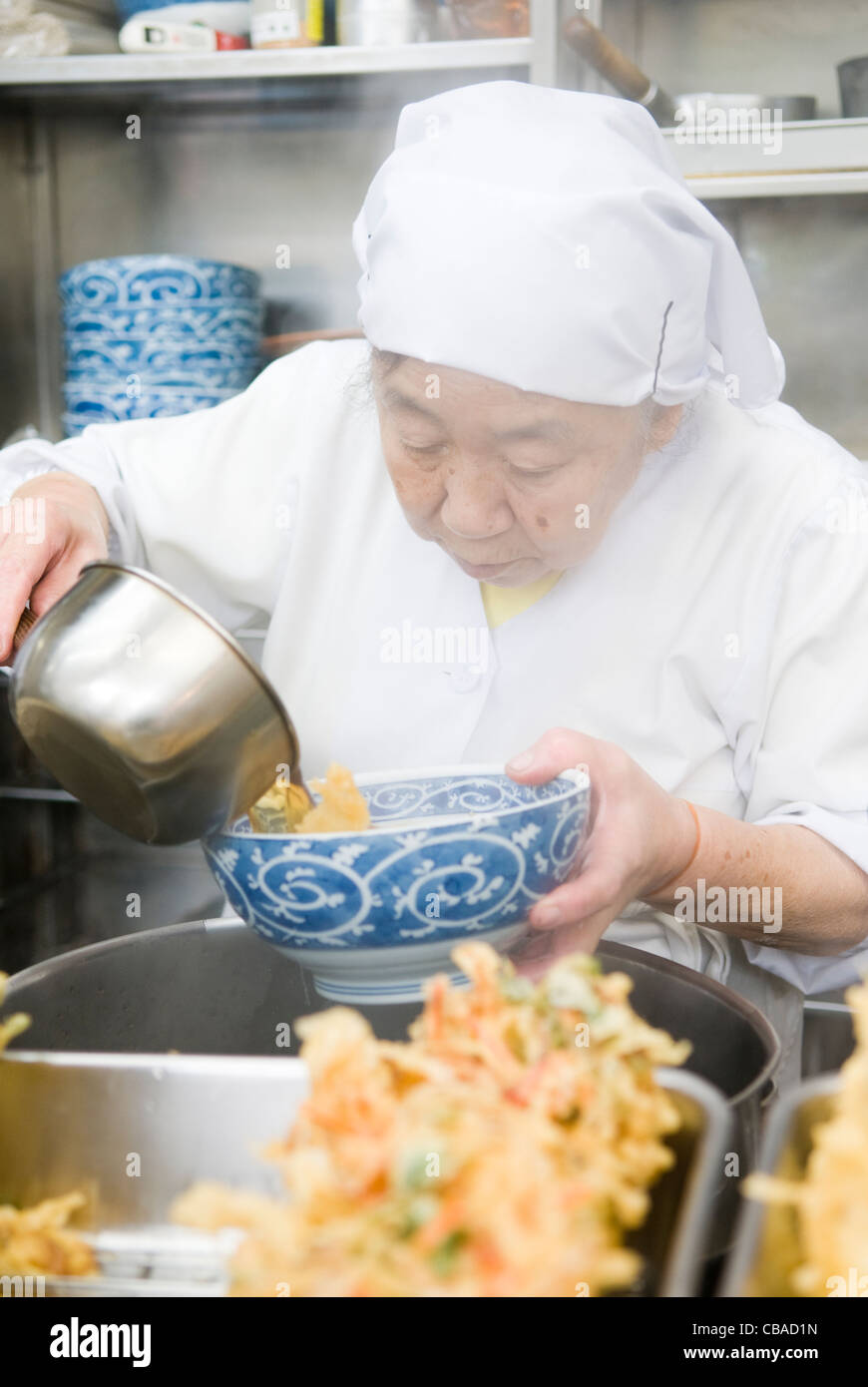 An old Japanese lady preparing home made tempura soba at a soba stall ...