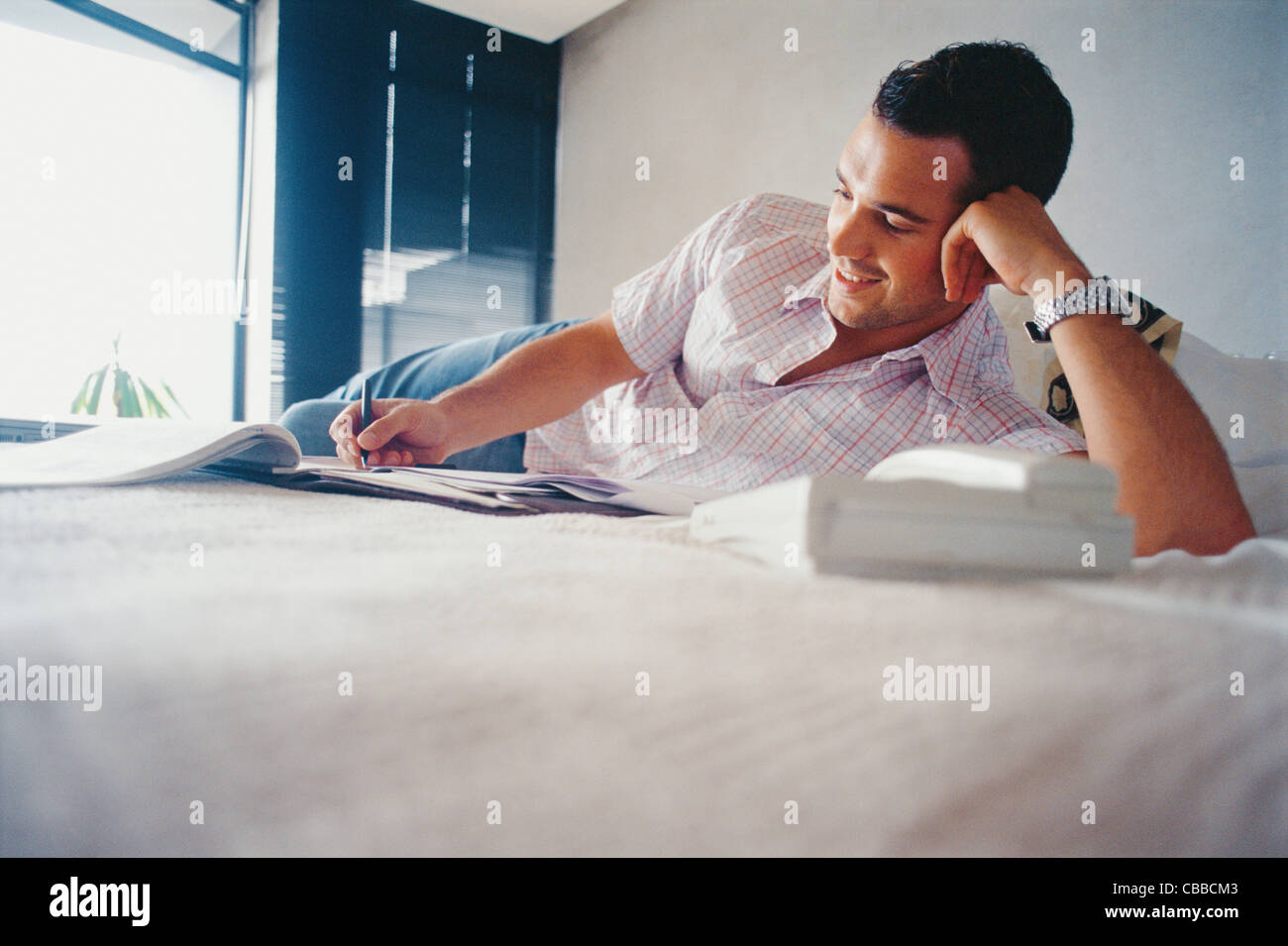 Smiling man writing on bed Stock Photo - Alamy
