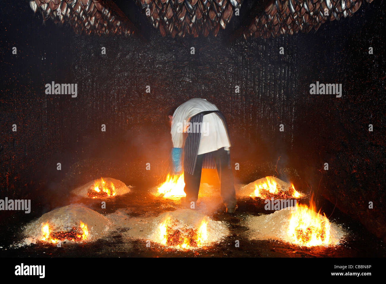 A man lights piles of wood chippings and oak sawdust in a smoking kiln ...