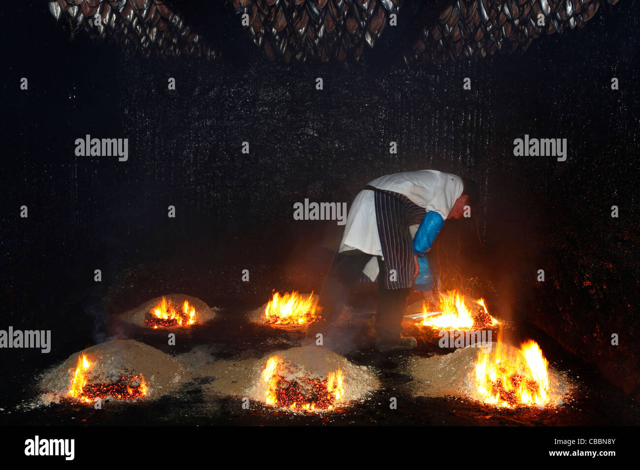 A man lights piles of wood chippings and oak sawdust in a smoking kiln ...