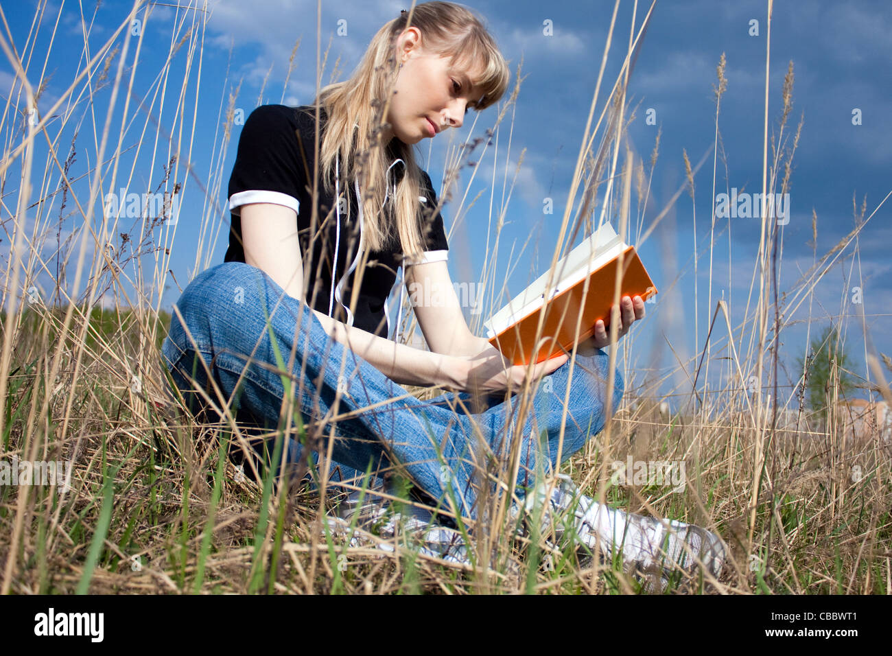 girl reading book and sitting outdoor with sky in background Stock ...