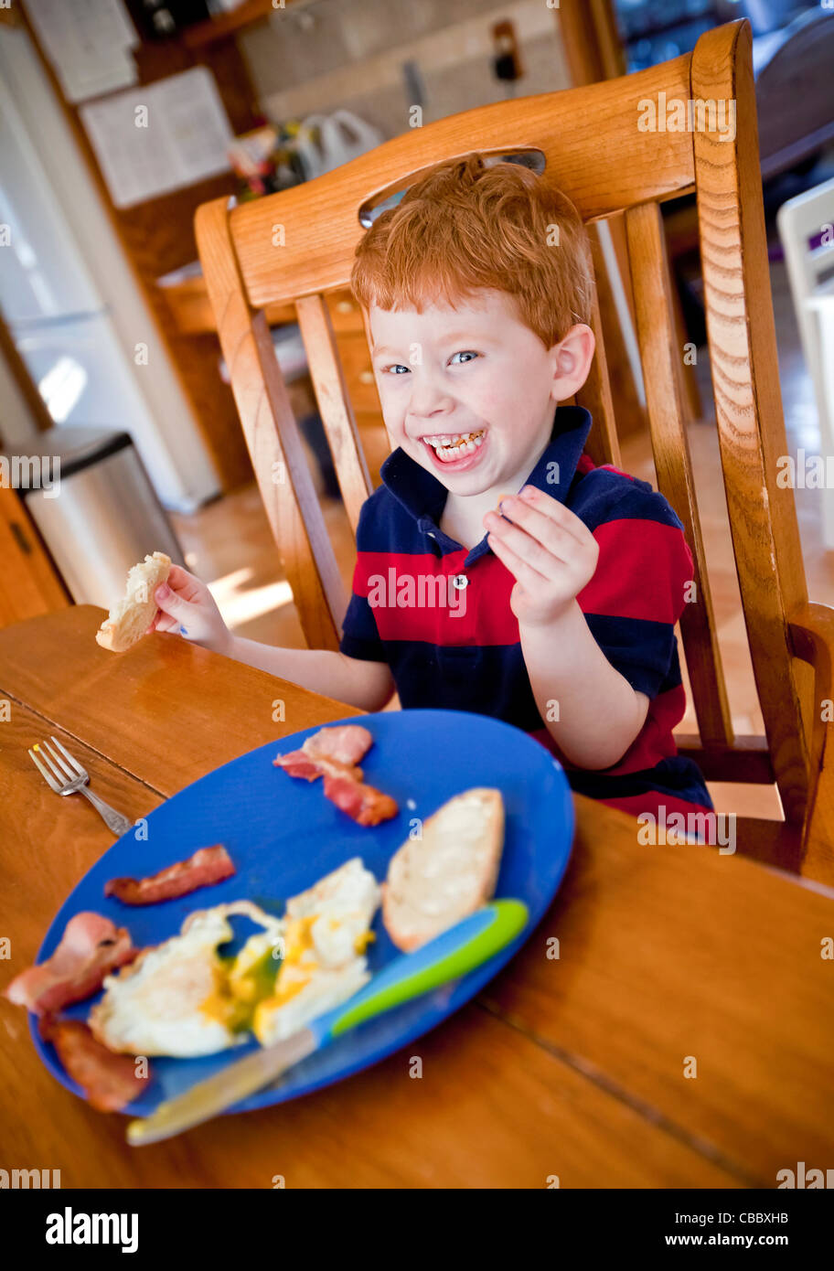 Happy redhead boy eating bacon and eggs at a table Stock Photo - Alamy