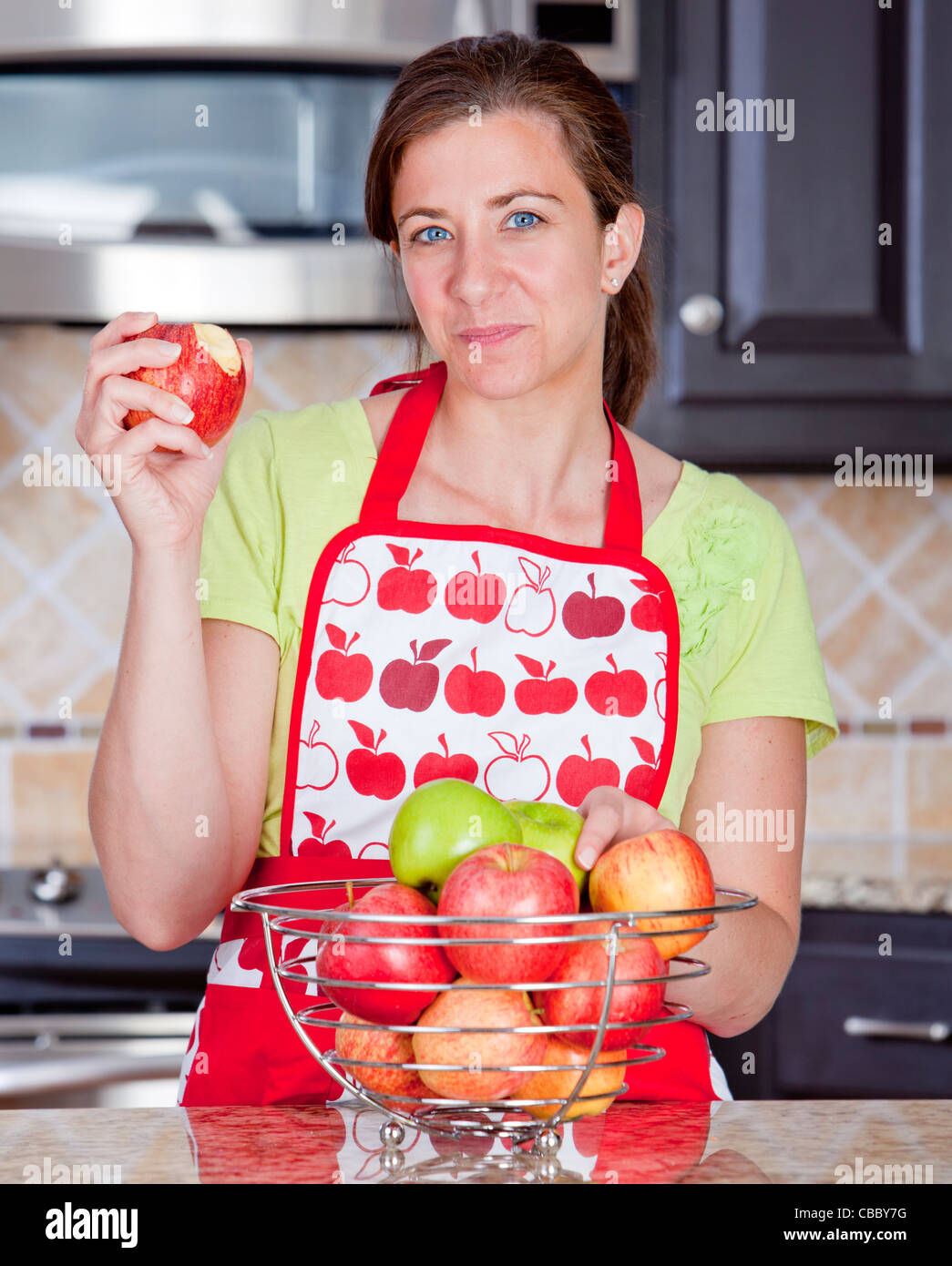 Pretty woman wearing an apron eating an apple Stock Photo - Alamy