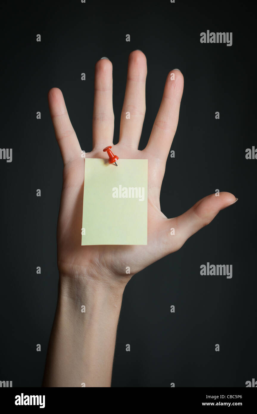 female hand with sticky office note nailed to hand with red pin. Note ...