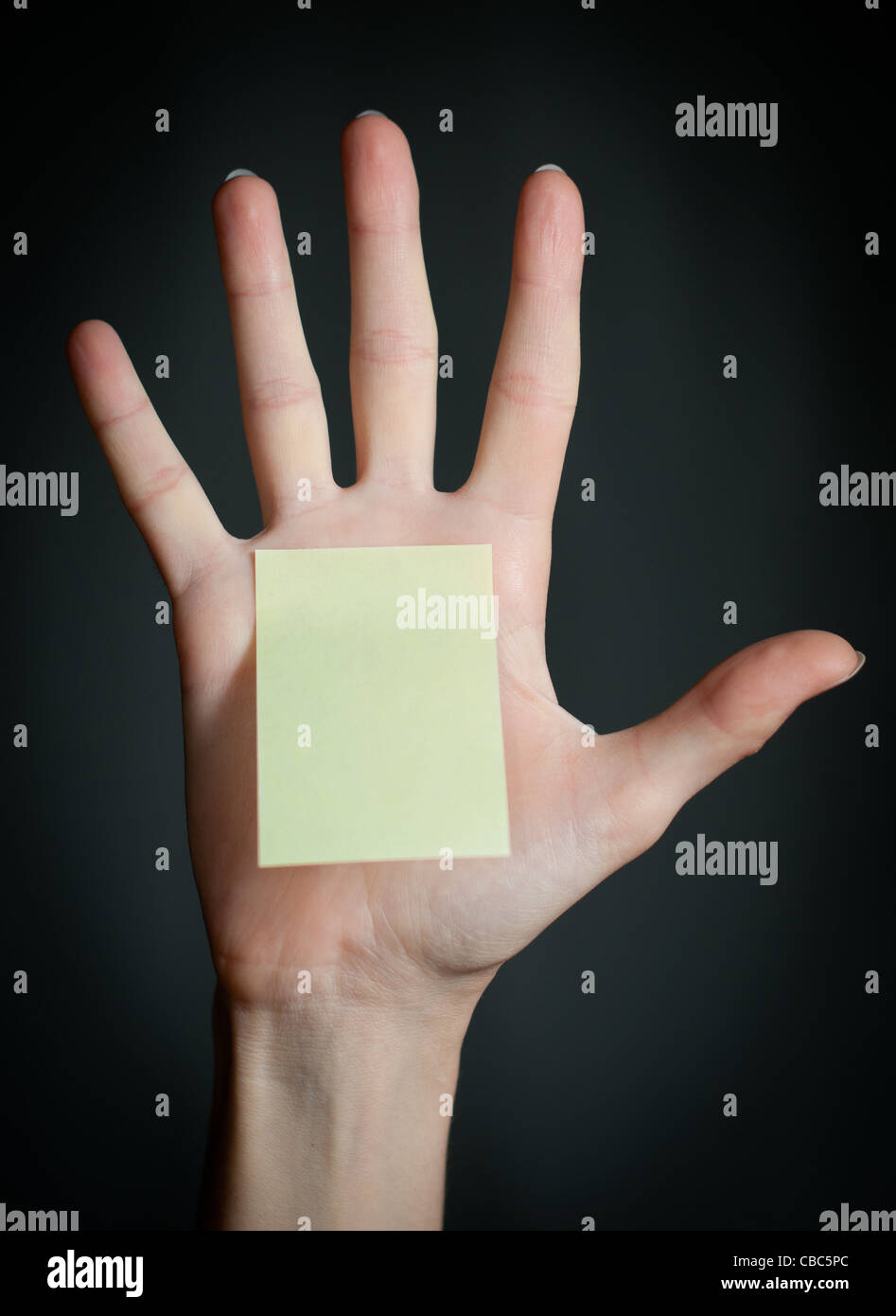female hand with sticky office note on dark background . Note is blank ...