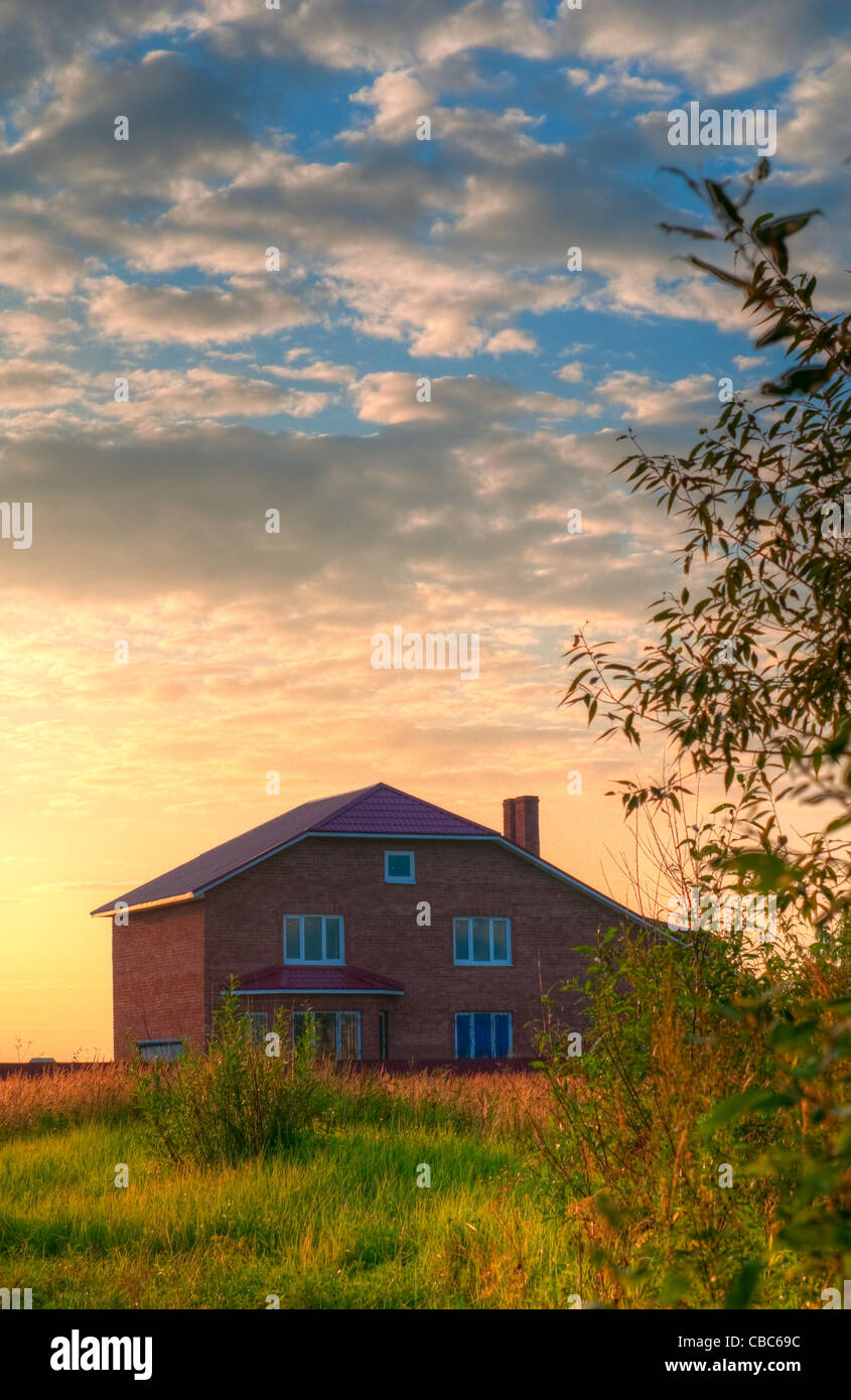 red brick house in the field of yellow flowers with cloudy sky in ...